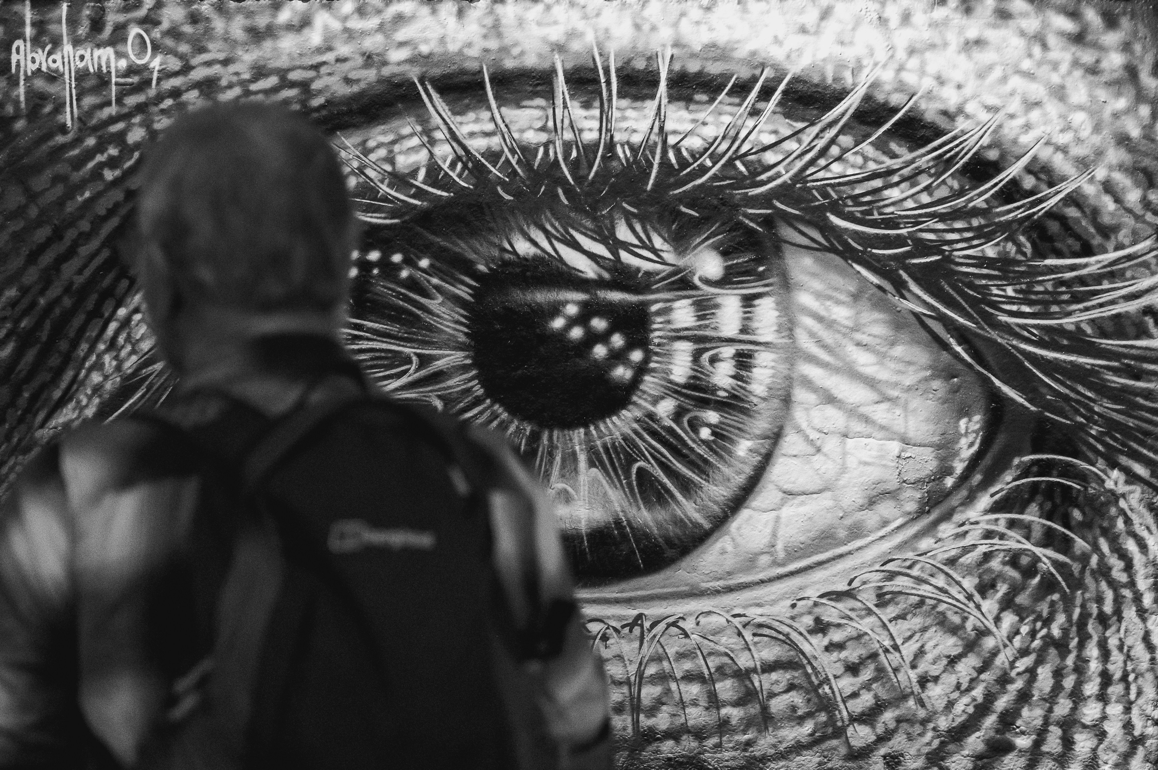 Macro-style close-up of a human eye with a photographer silhouette in the foreground, emphasizing texture and detail; monochrome presentation.