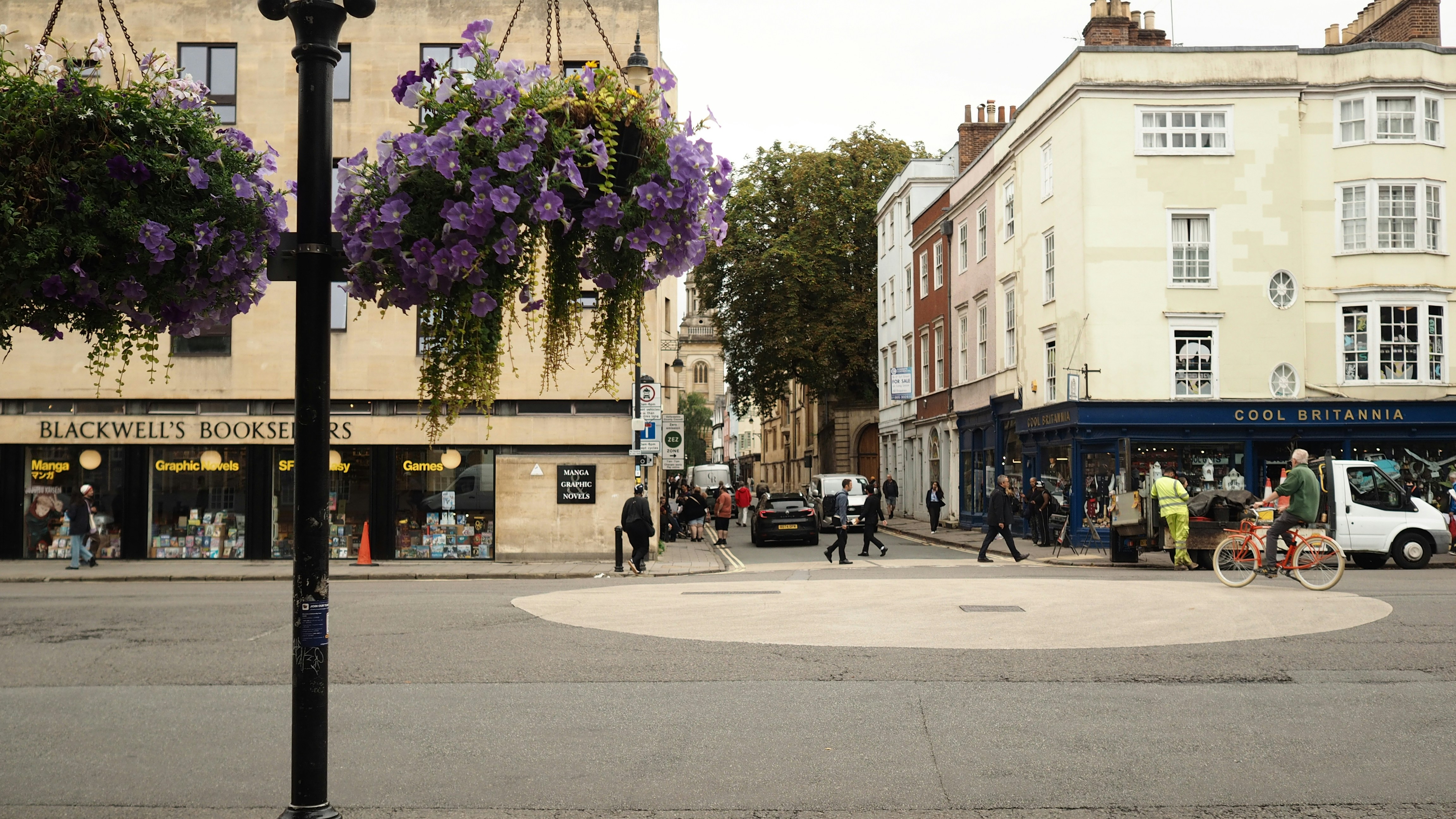 Town Square in Bloom: Pedestrians, Cyclist, and Bookshop Facade