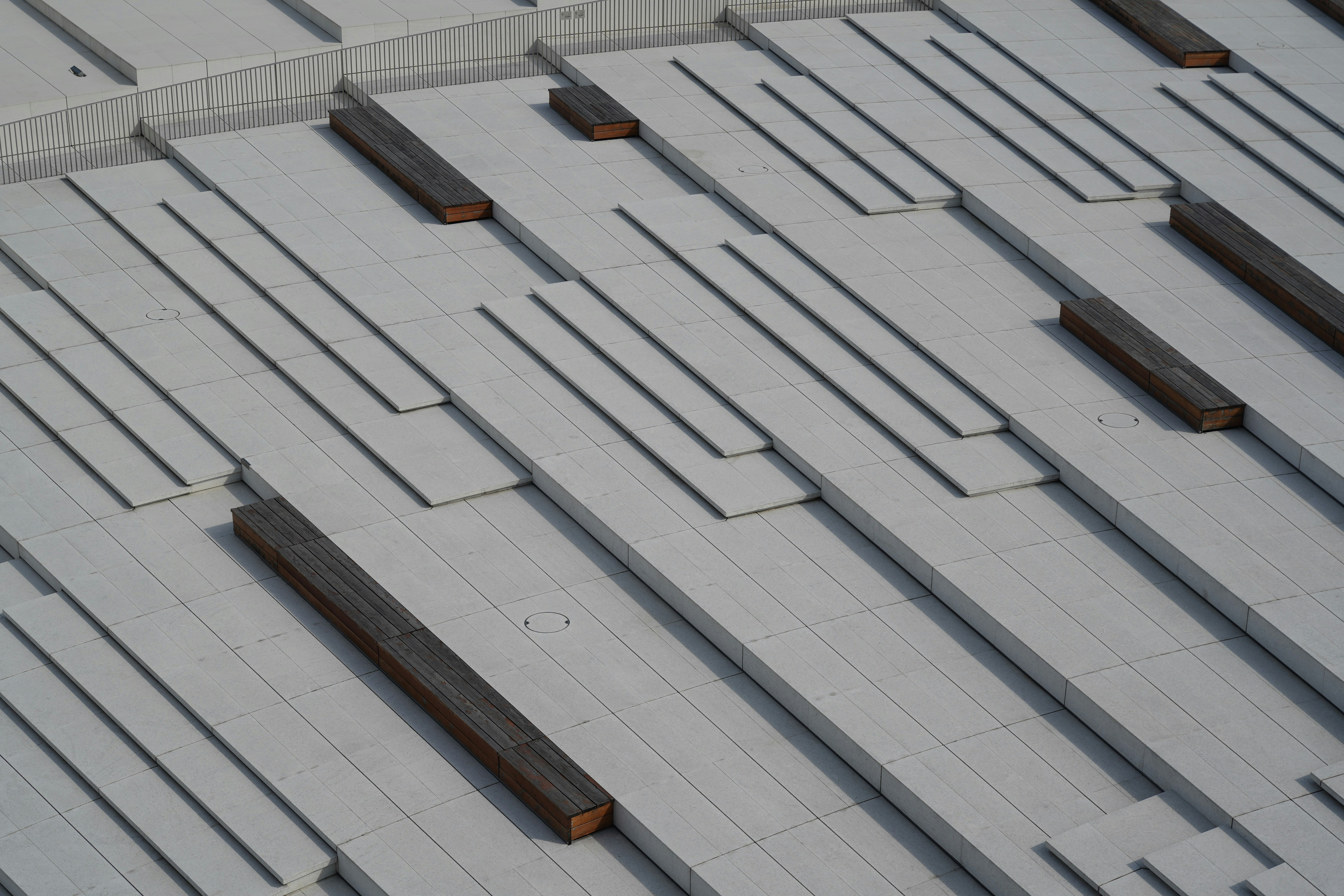 Geometric rooftop tiles create intersecting linear patterns and shadows, forming a maze-like surface with repeating rectangles and rusted accents.
