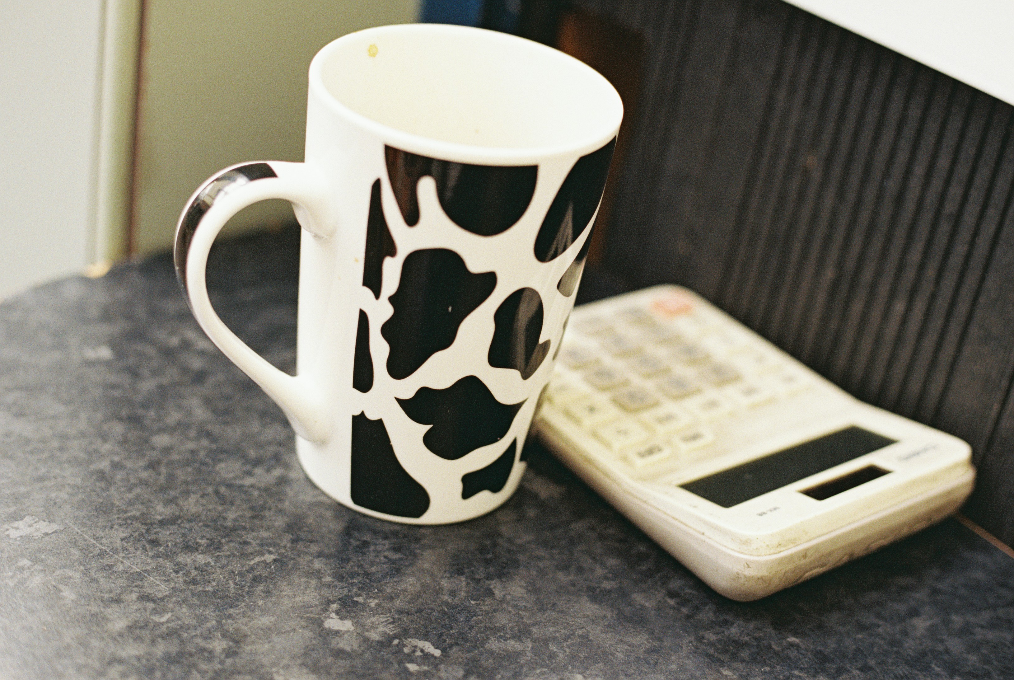 Monochrome mug with cow pattern resting beside a calculator on a speckled counter