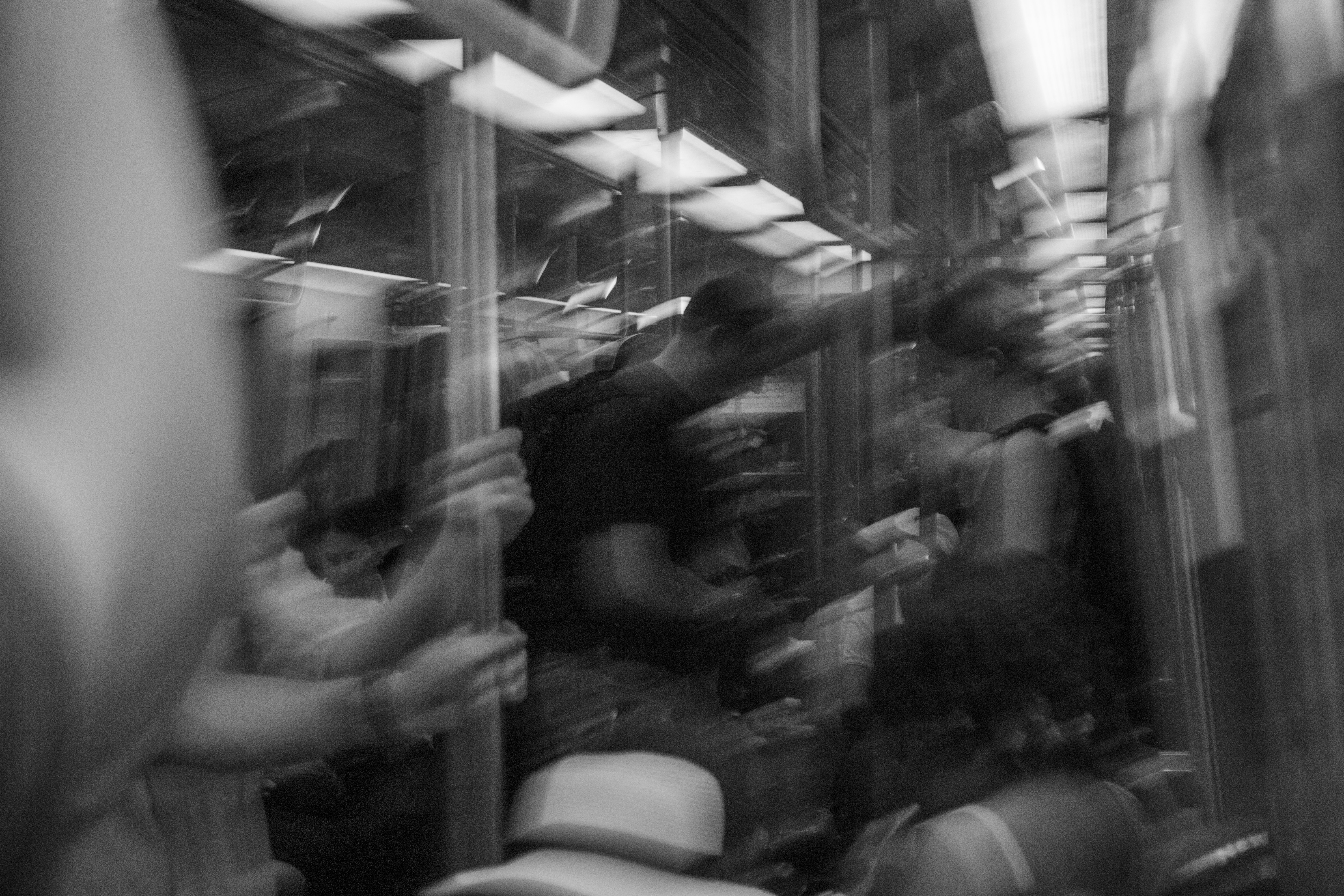 Black-and-white subway scene with motion blur and crowded interior, emphasizing transient human motion inside a train car.