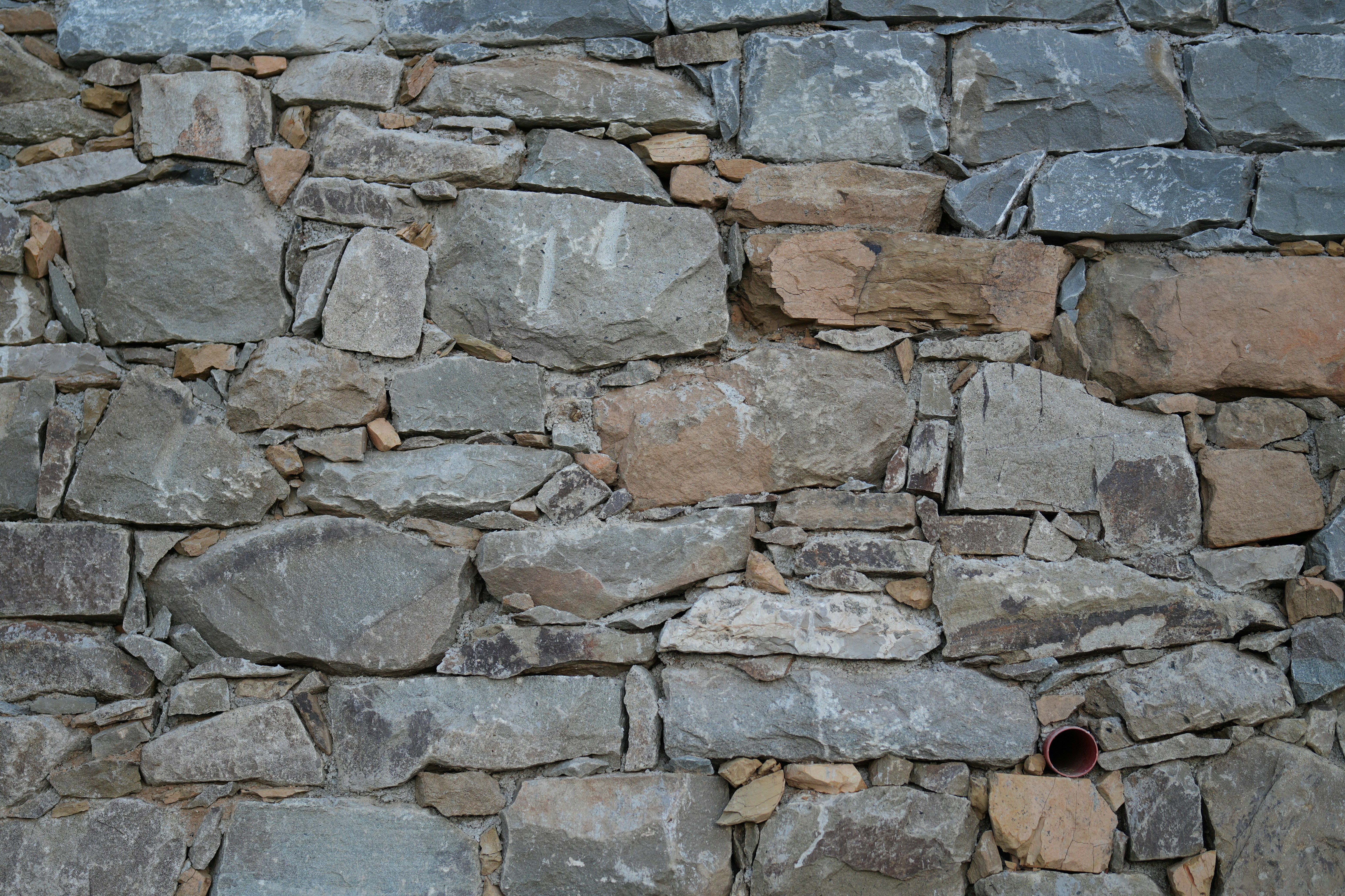 Stone Wall Mosaic: Subtle Red Pipe and Weathered Gravel
