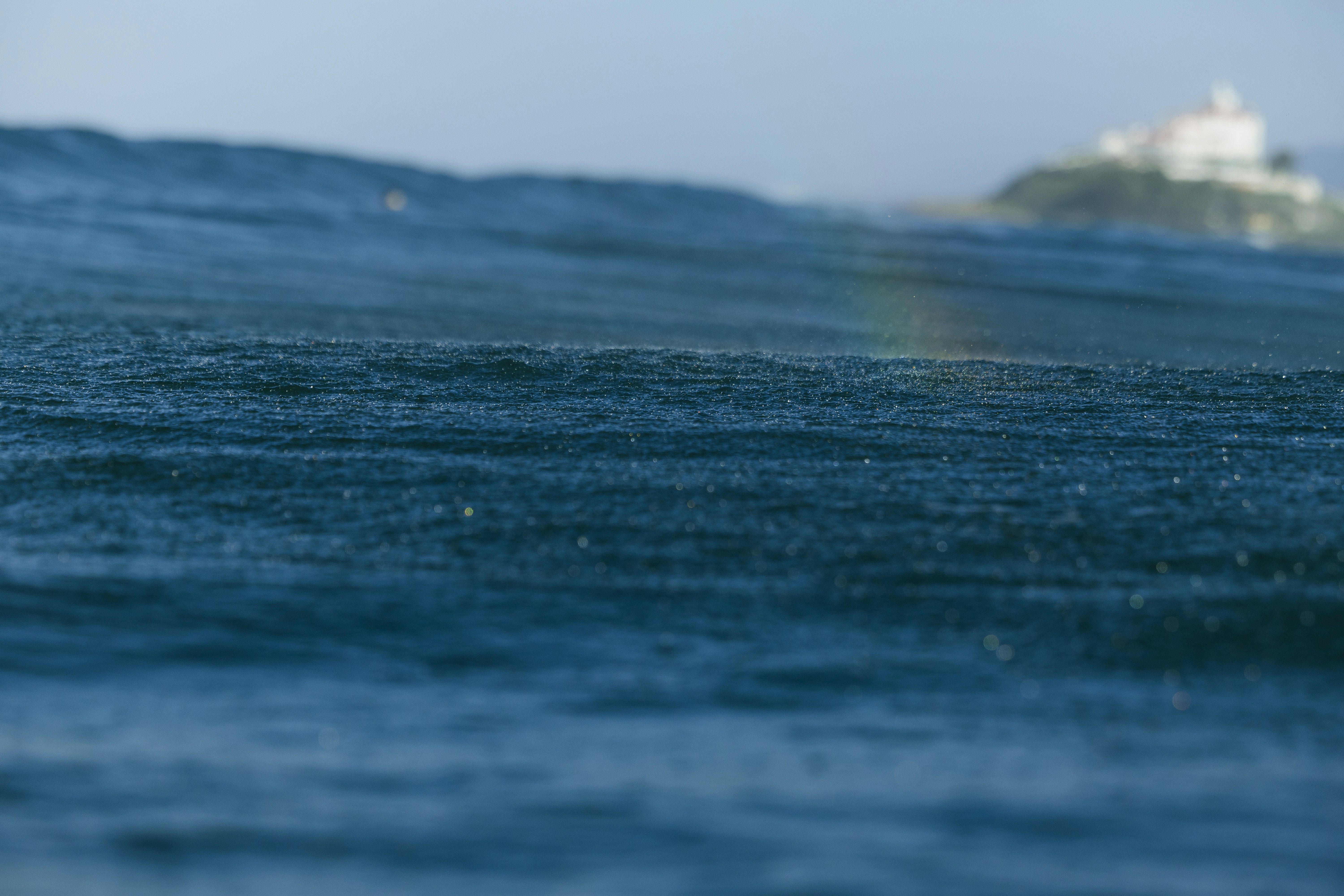 Expansive ocean surface with a distant, softly lit horizon and a faint structure at the far right. The image emphasizes wide-angle water texture and tranquil depth.