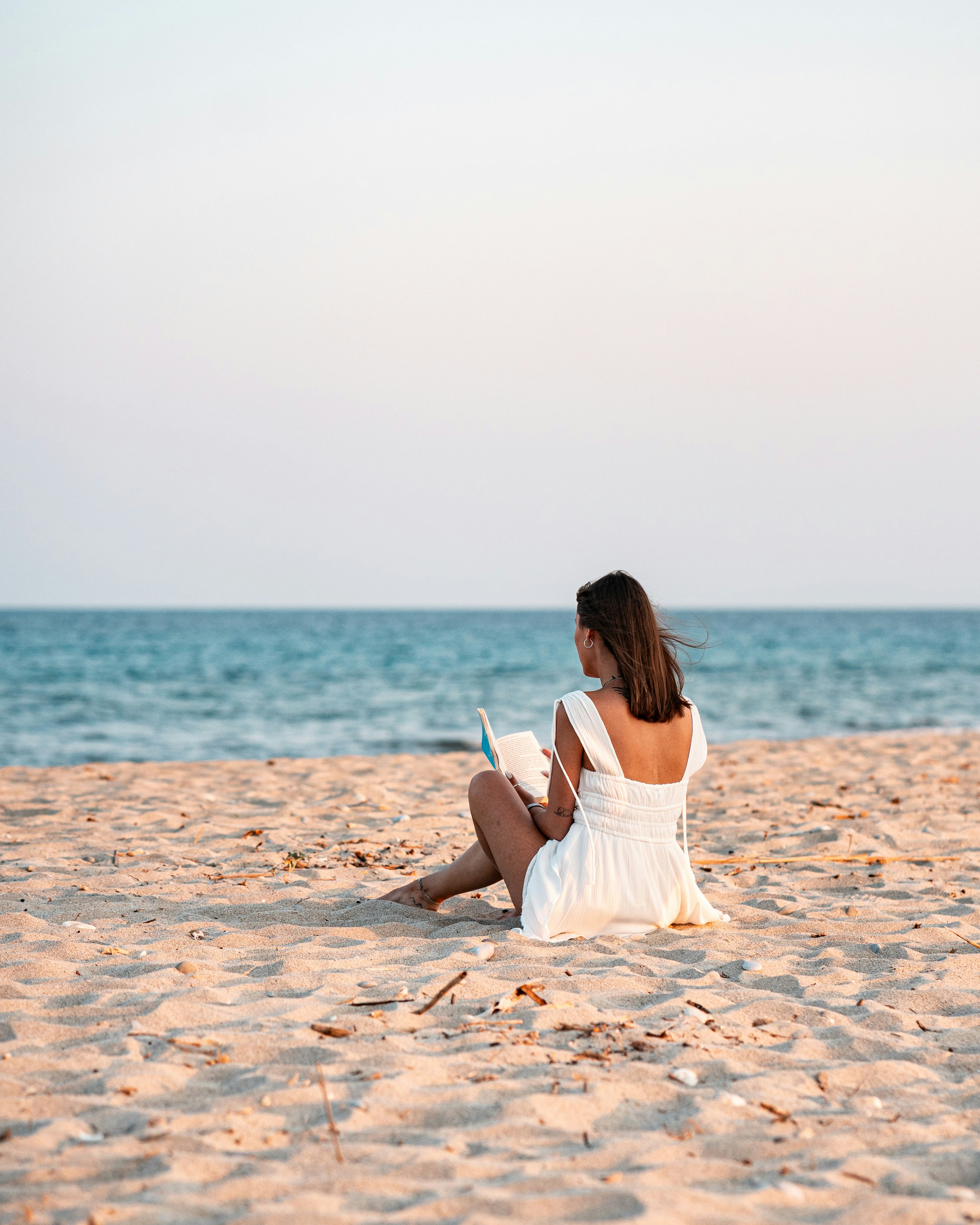 Sandy Solitude: A Seated Reader by the Ocean