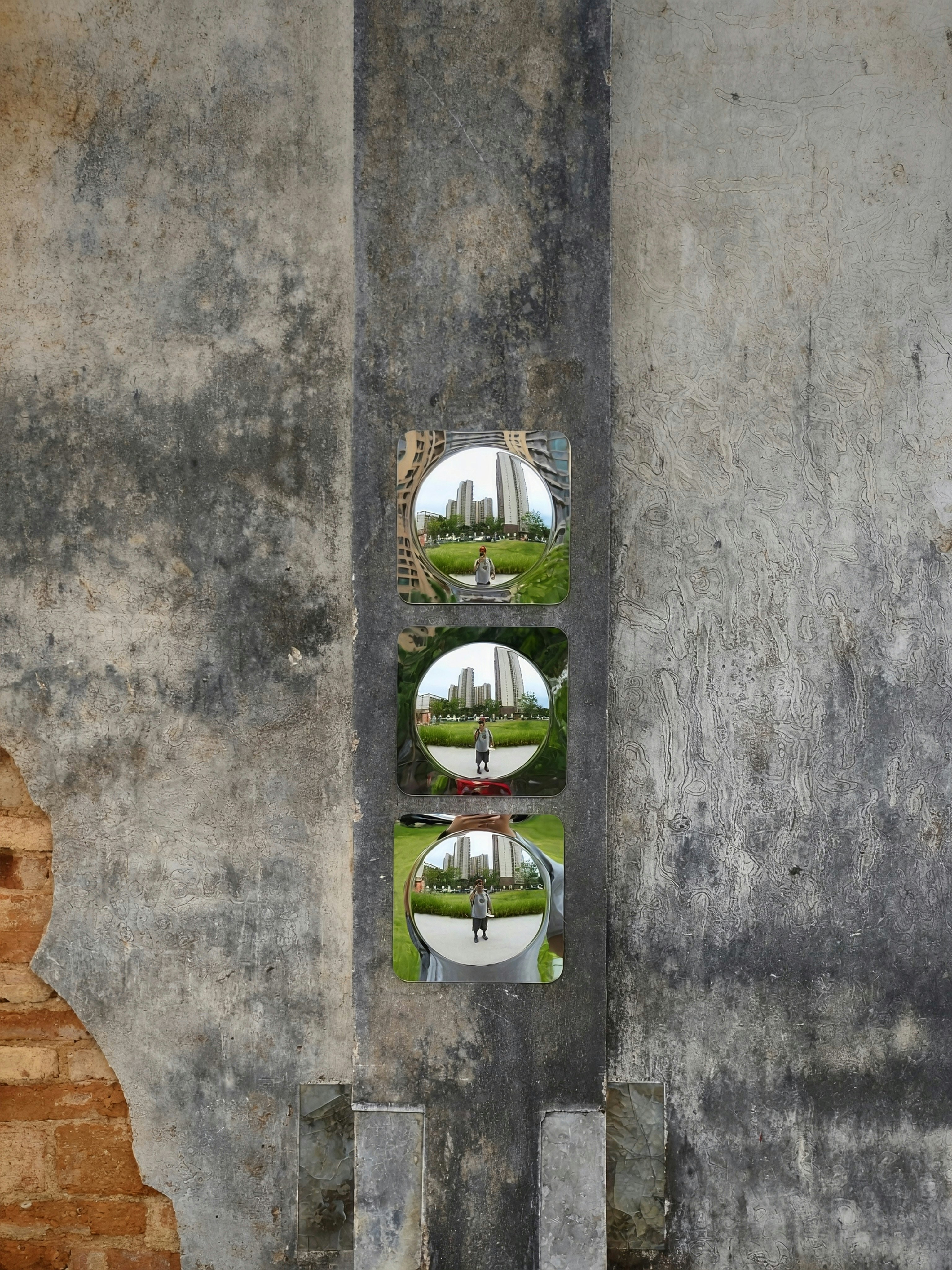 Three circular convex mirrors reflecting a person and buildings on a weathered concrete wall
