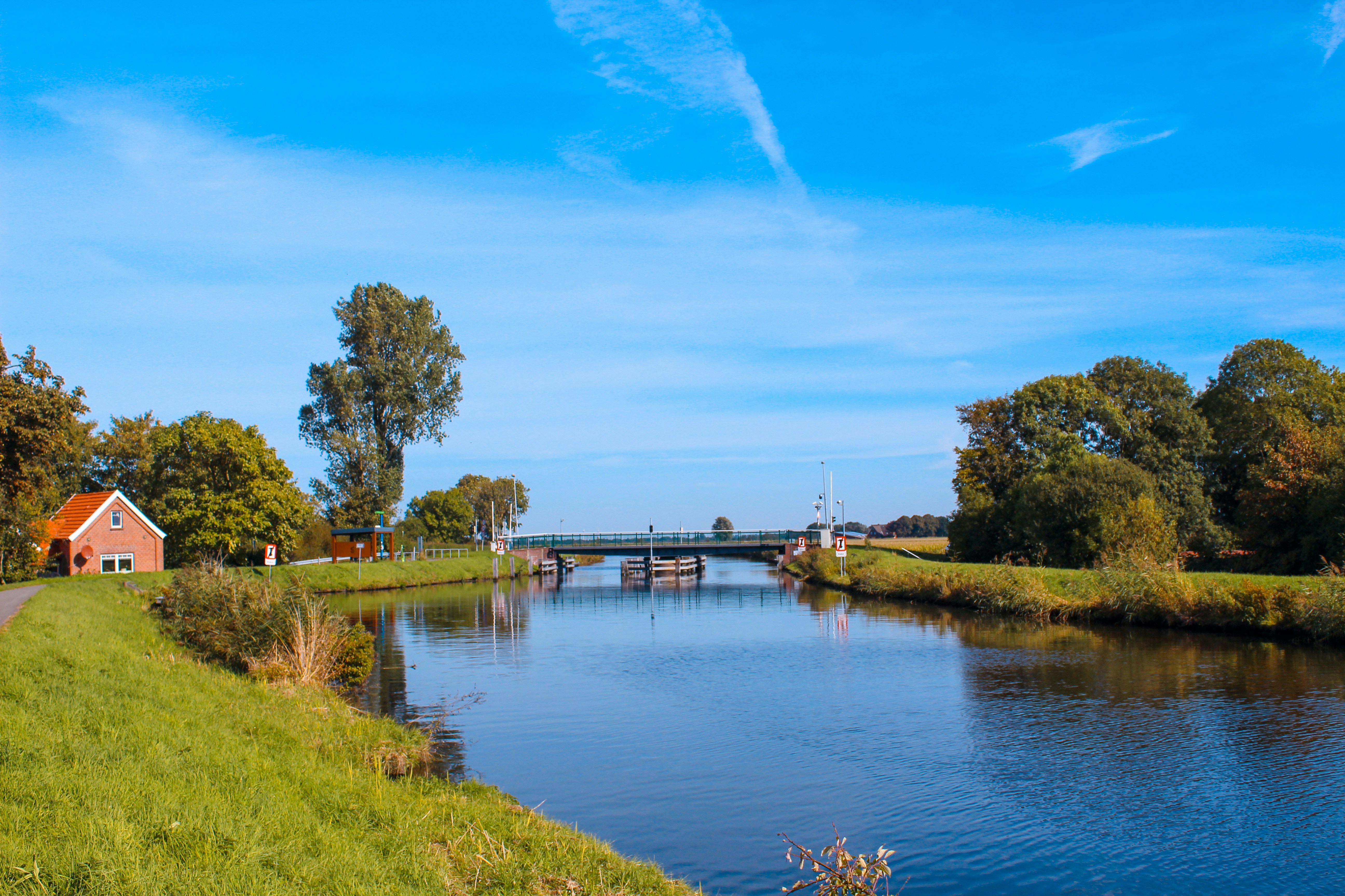 Riverside Lane: Bridge, House, and Willow Trees Framing a Calm Waterway
