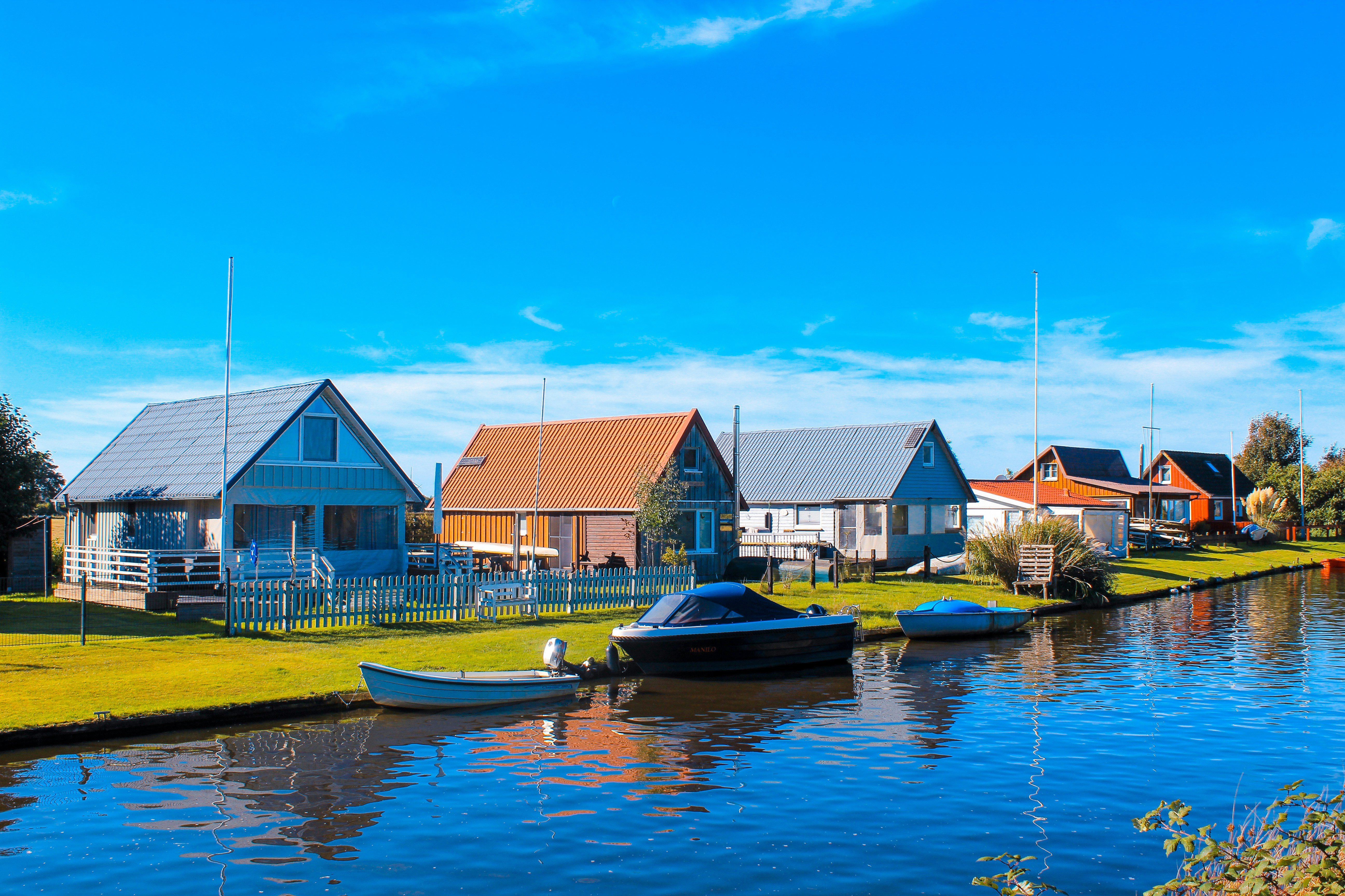 Vibrant houses line a canal with small boats resting along a grassy bank, under a bright blue sky.