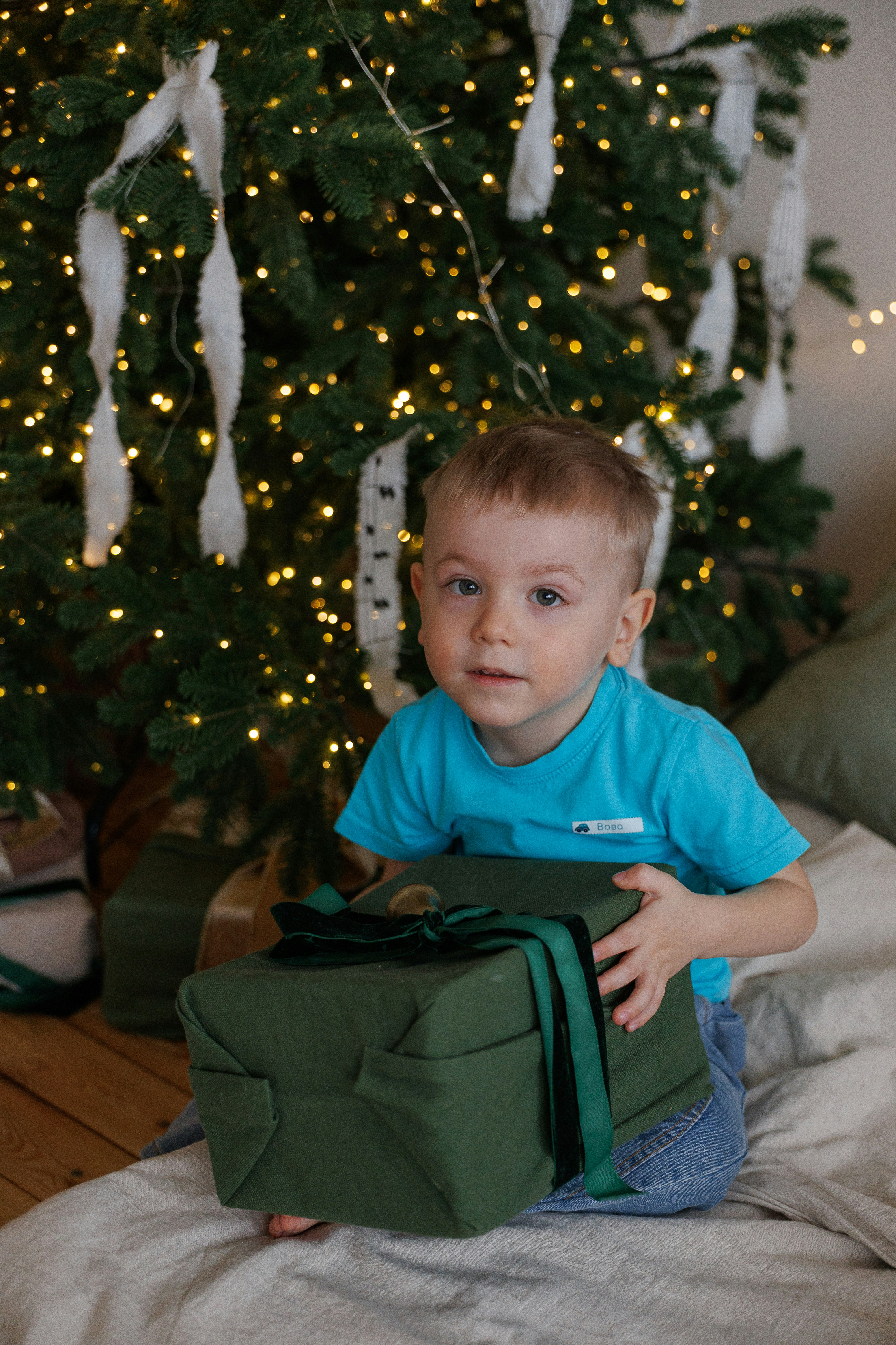 A young child with a gift under a softly lit Christmas tree