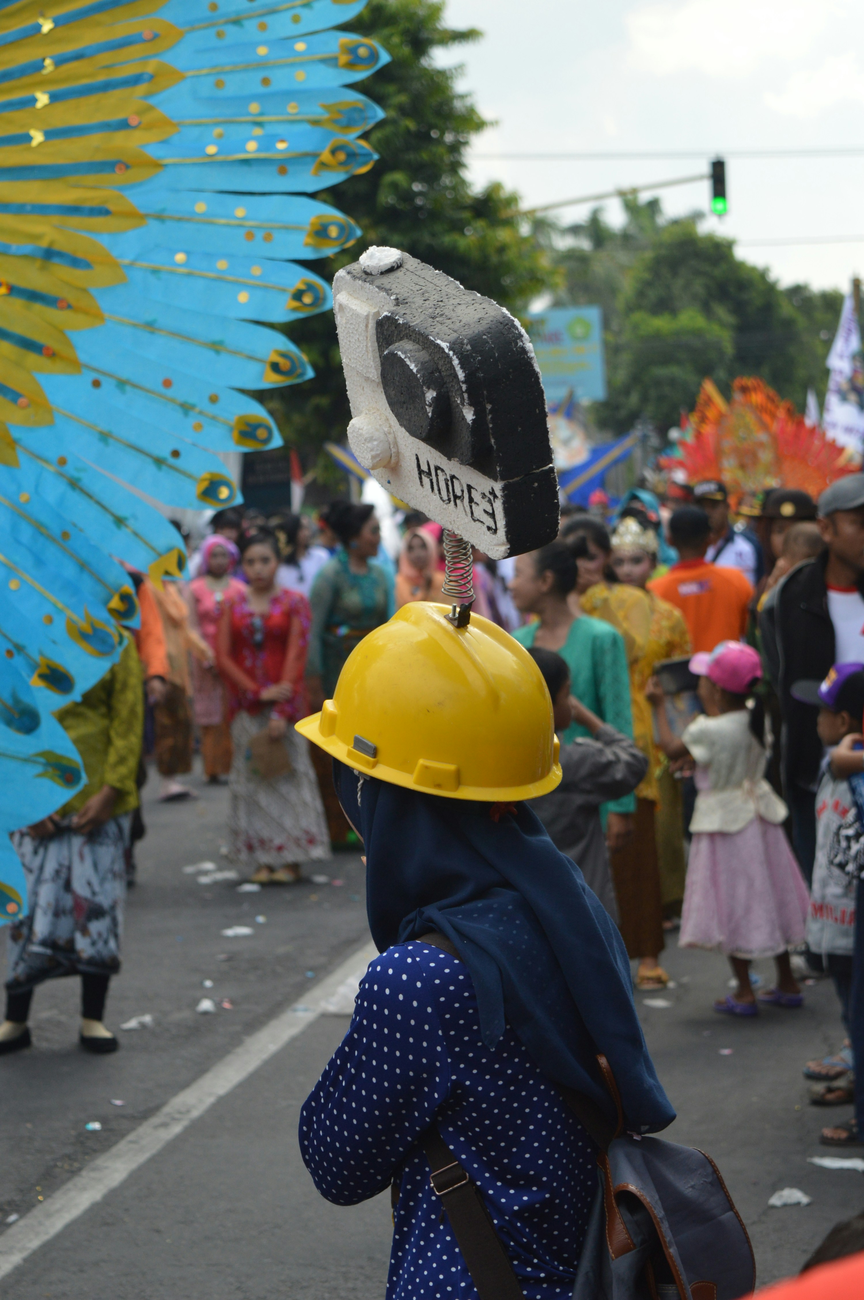 Yellow helmet, suspended hammer, and festival crowd: a street-side moment in motion