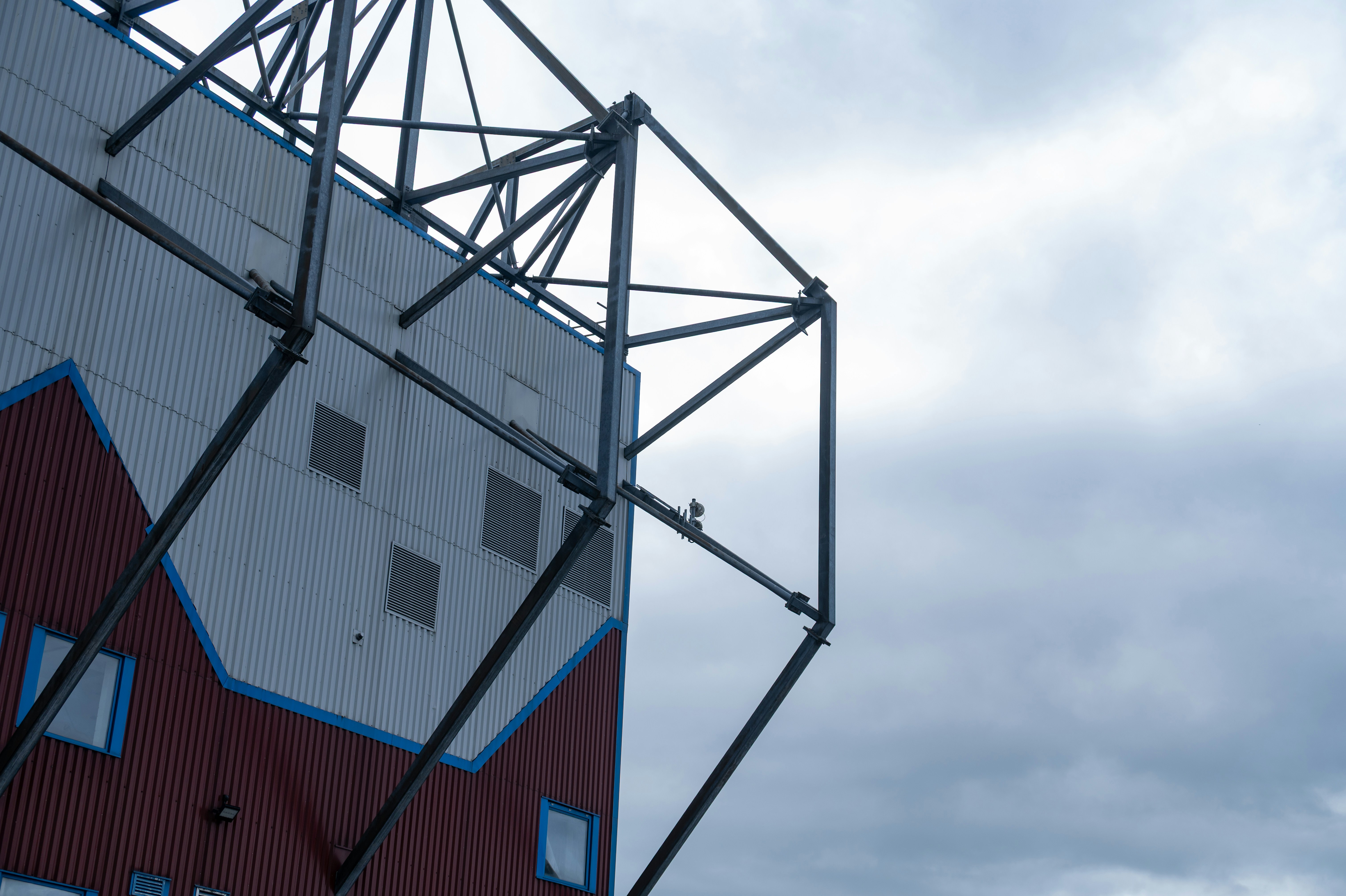 Red-and-blue corrugated building with exposed steel framework against a moody sky; emphasis on architectural lines and industrial texture.