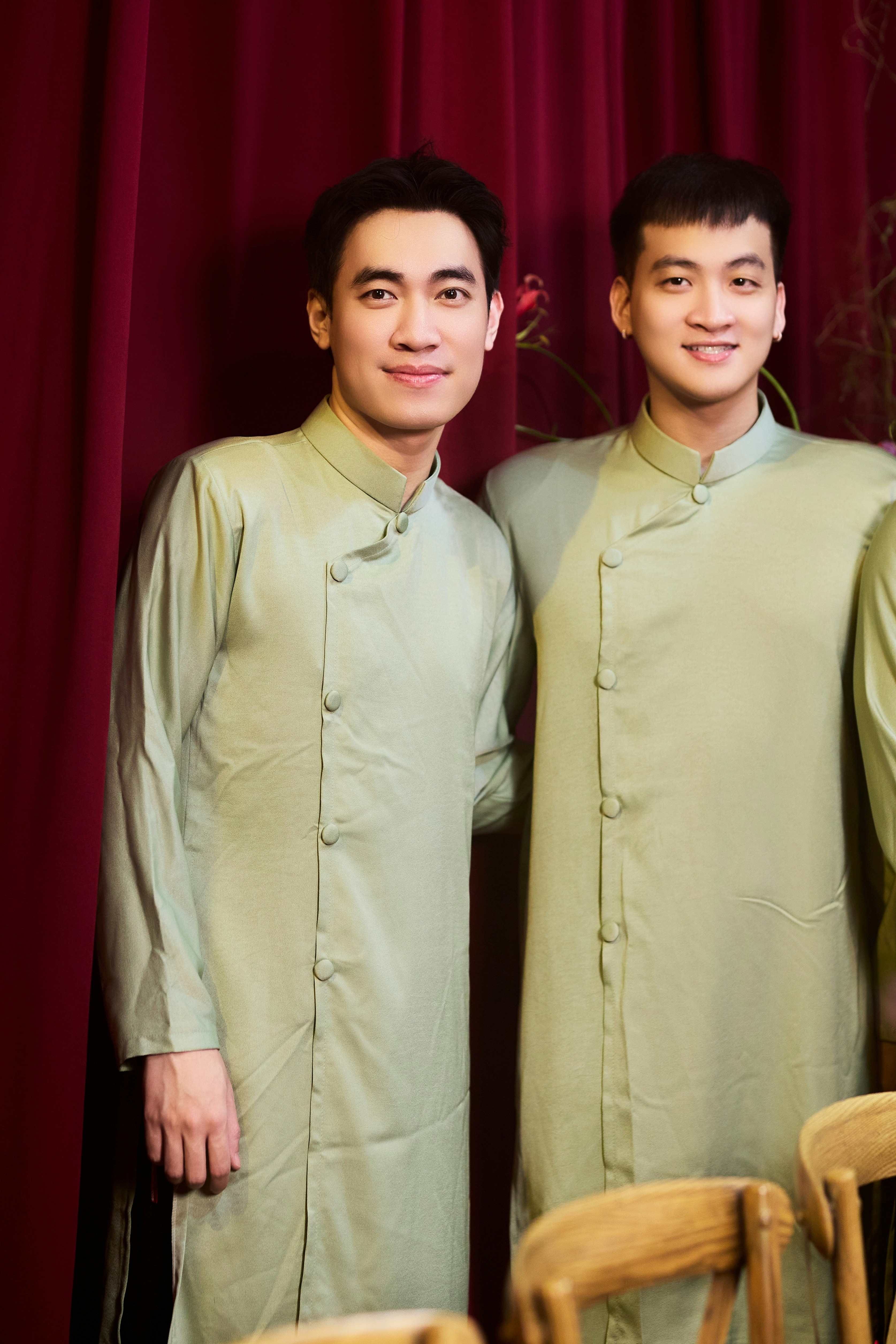 Twin smiles in matching sage garments under velvet drapes