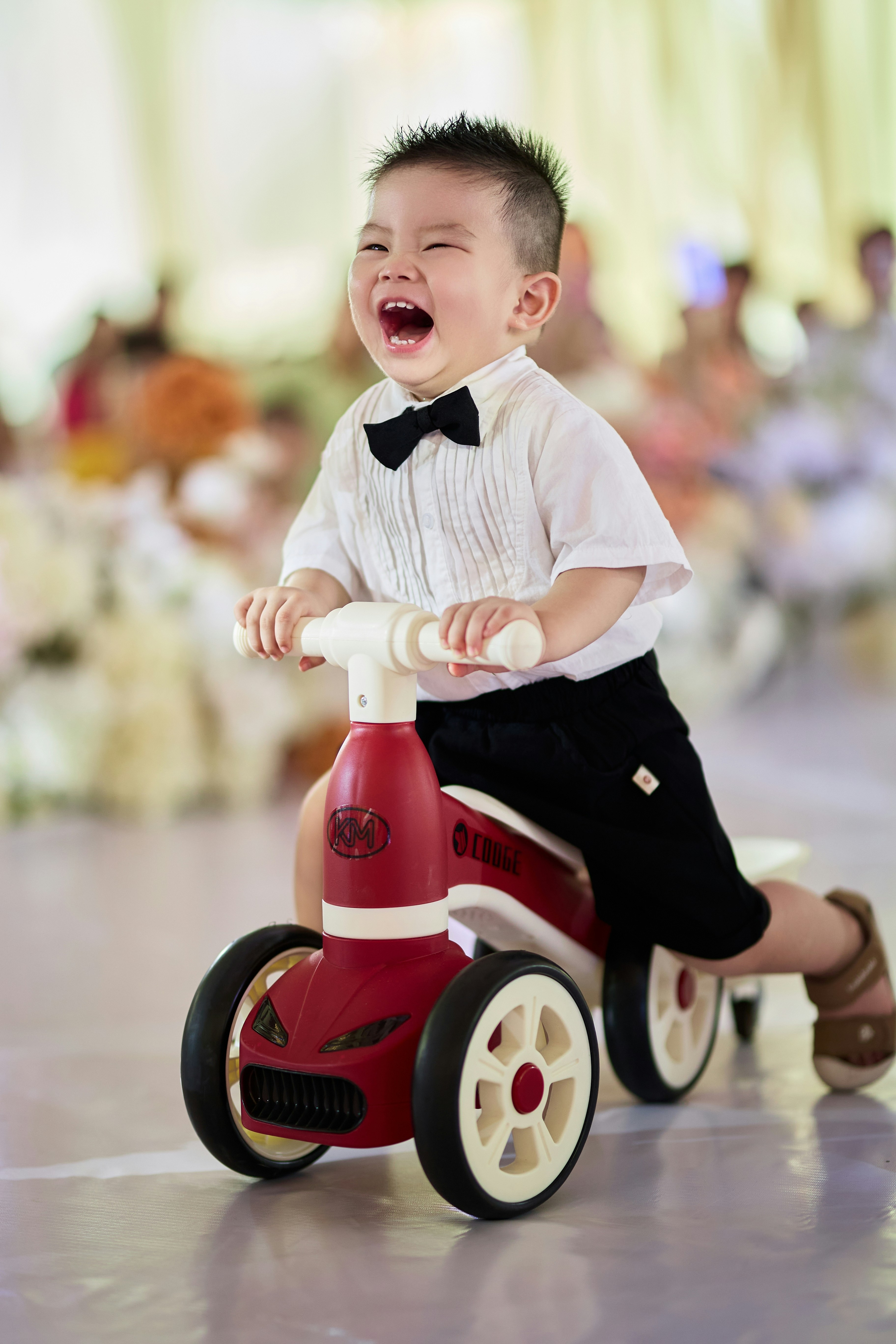 Joy in Motion: Baby on a Red Trike at a Soft-Focus Party