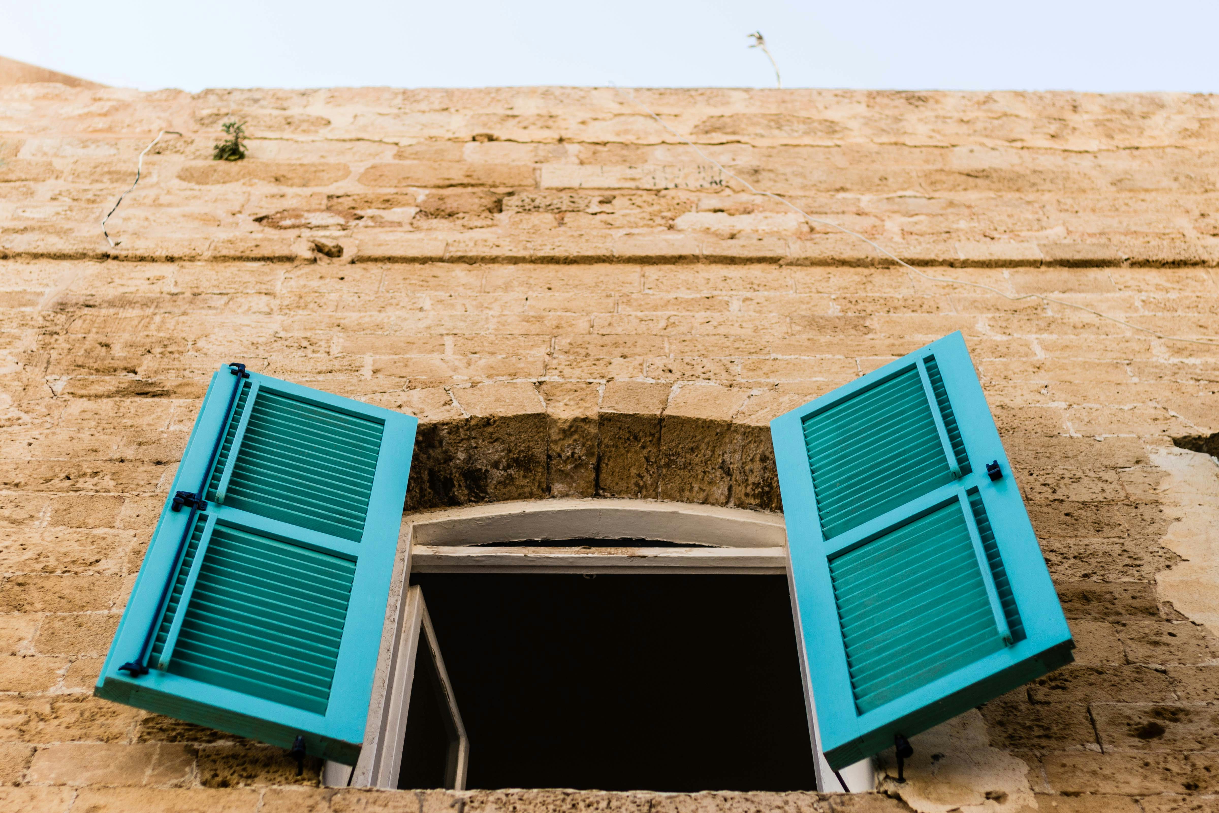 Turquoise Window Shutters in a Sunlit Brick Facade