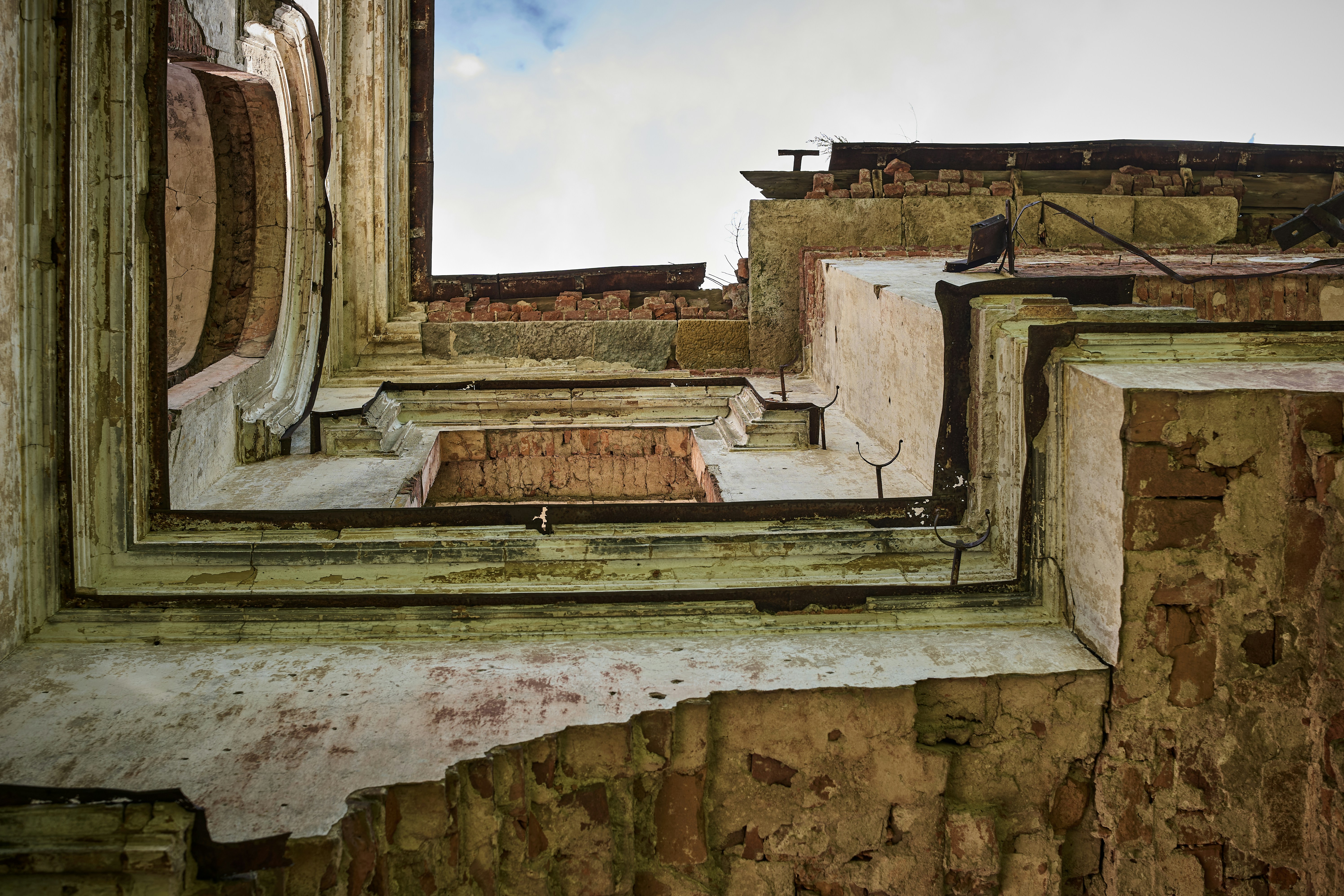 An upward view of weathered building edges and architectural recesses, with a sliver of blue sky visible above; the textures and peeling plaster emphasize age and geometry. (Photo, not a painting or illustration)