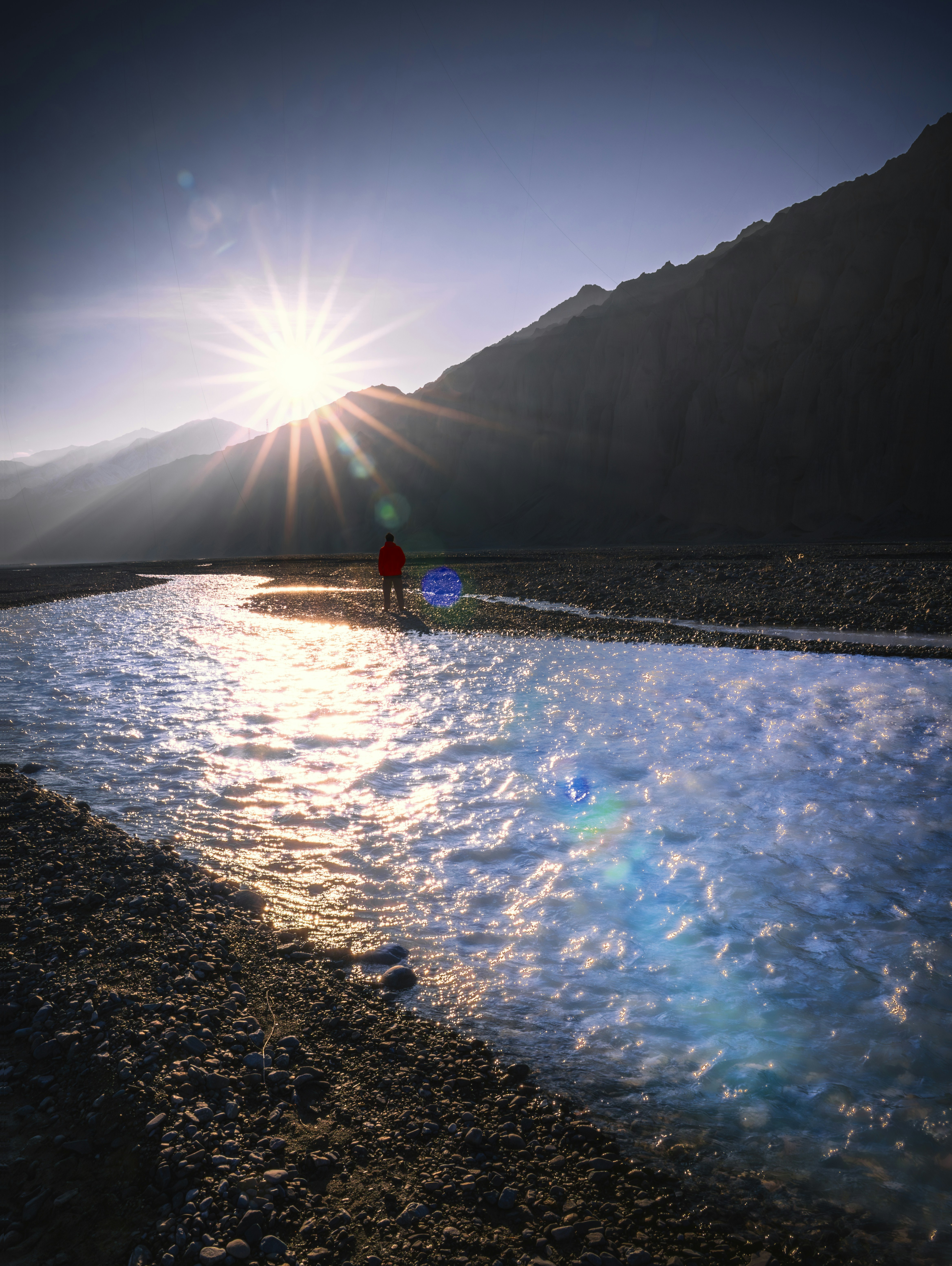 Sunlit solitude by glacial stream with a lone figure