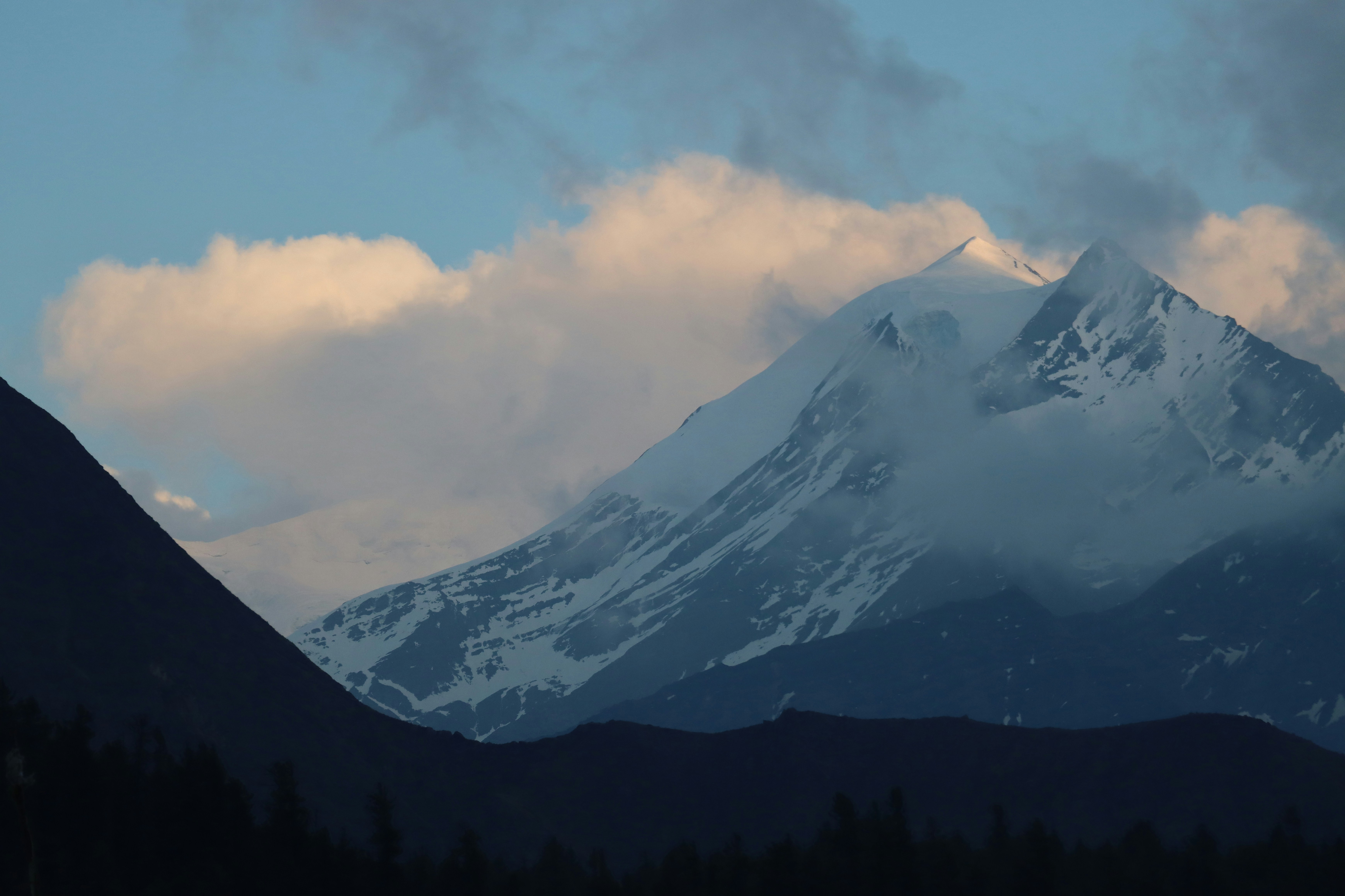 Snow‑capped peak peeking through a veil of clouds at dusk