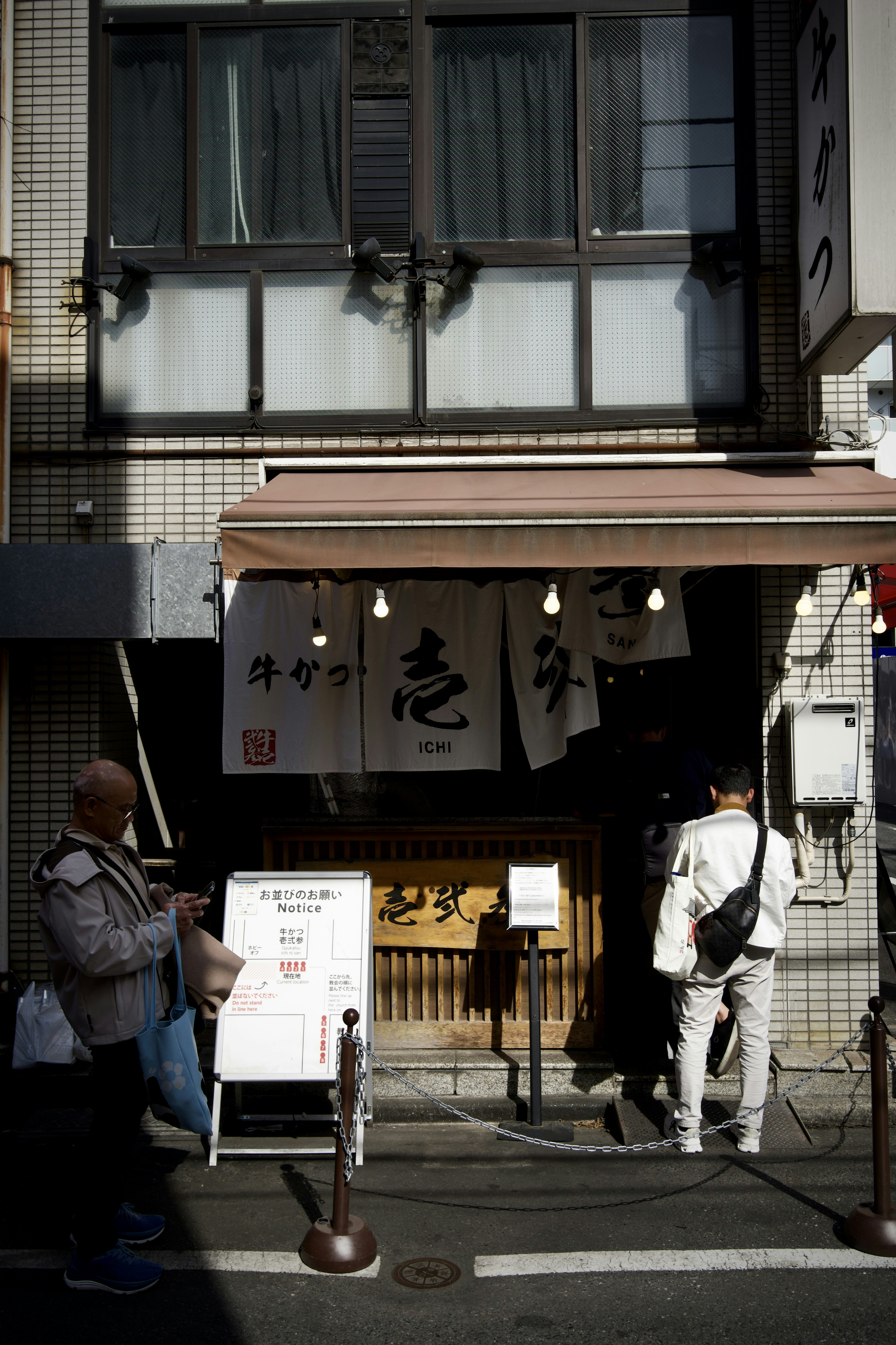 Entrance to a Japanese eatery: fabric banners, warm light, and patrons at the doorway