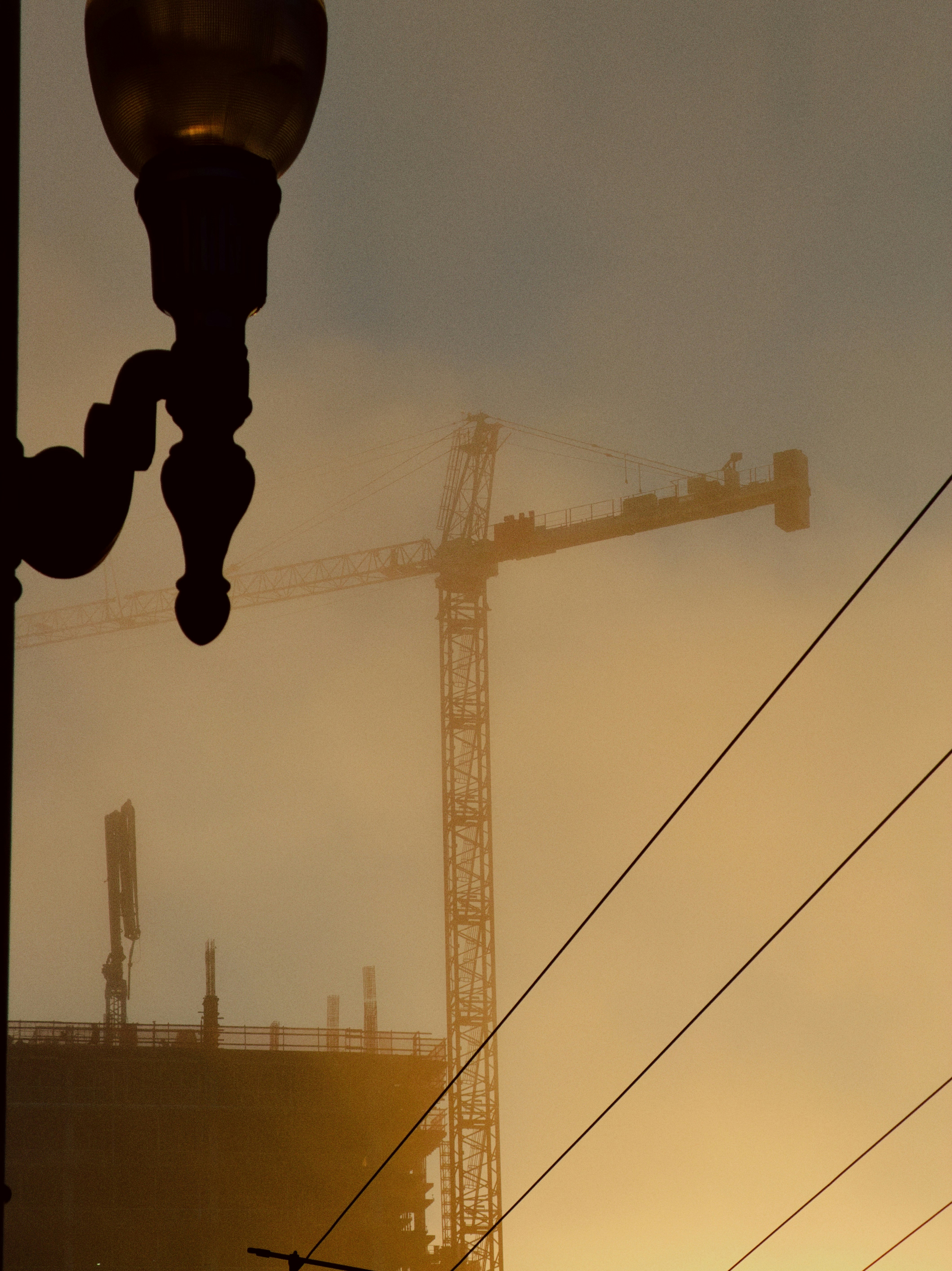 A construction crane and building silhouette against a hazy golden sky