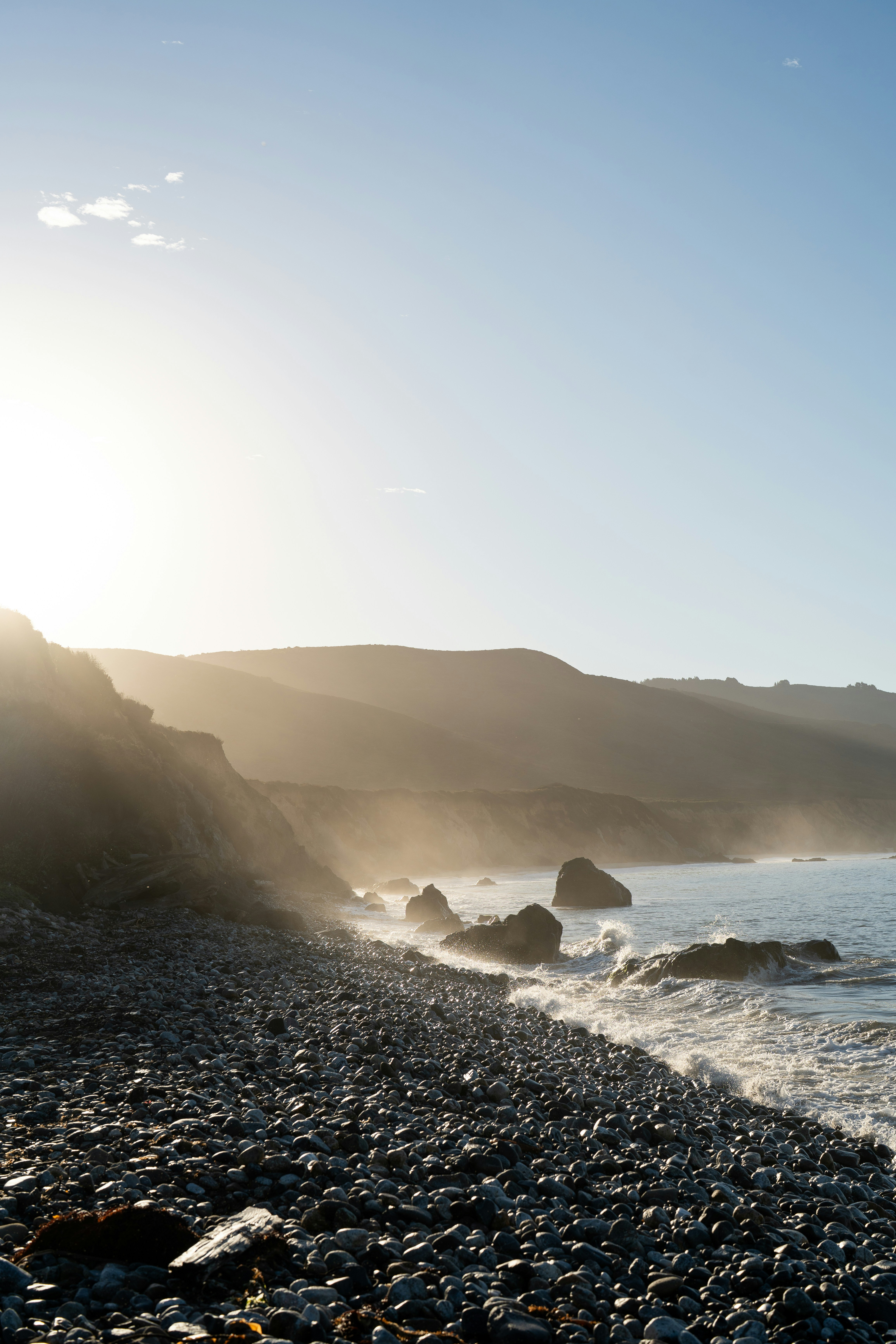 Dawn over a pebble shore: sunlit mist and rugged coastline
