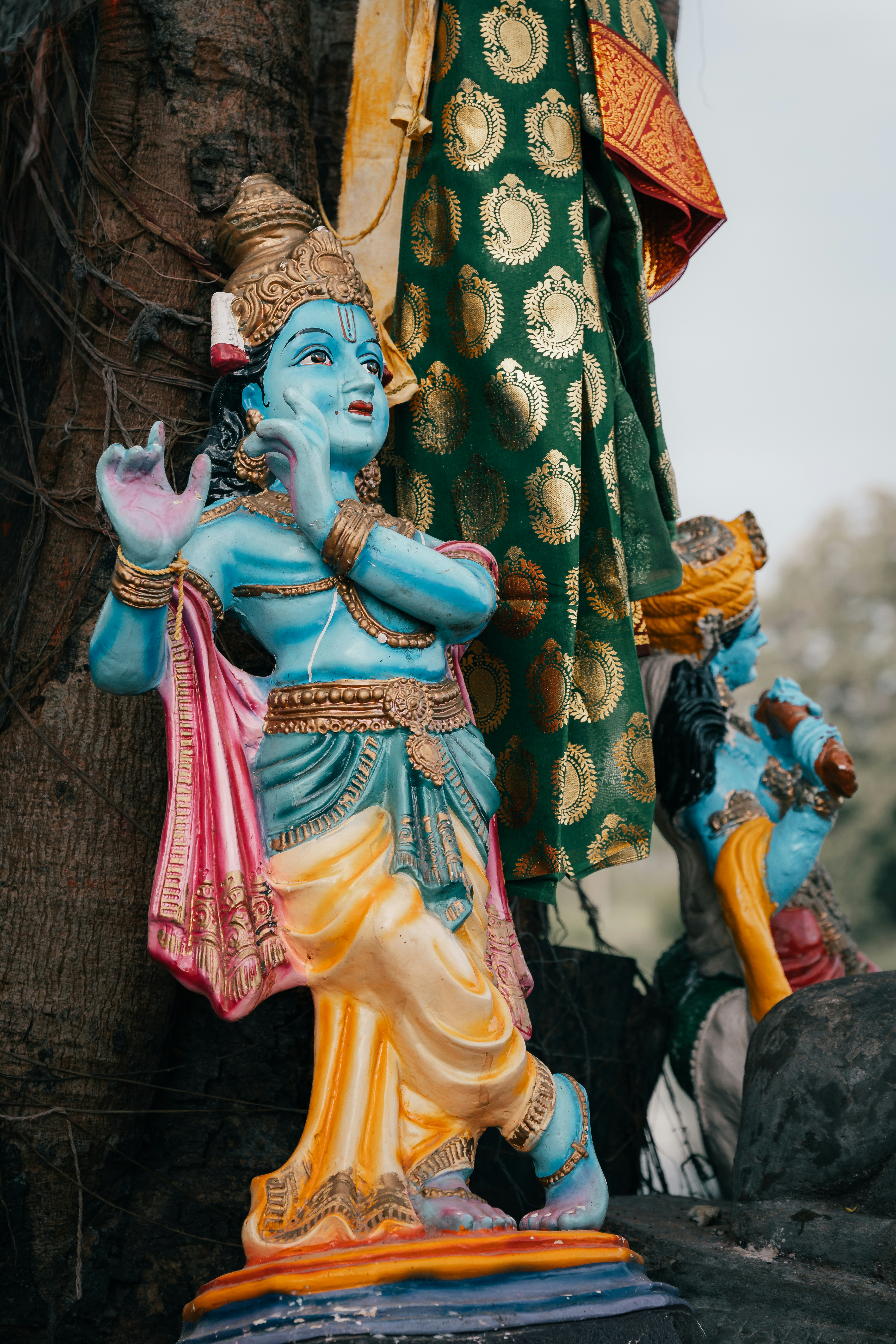 Blue Hindu Figure in Colorful Attire Waving by a Tree