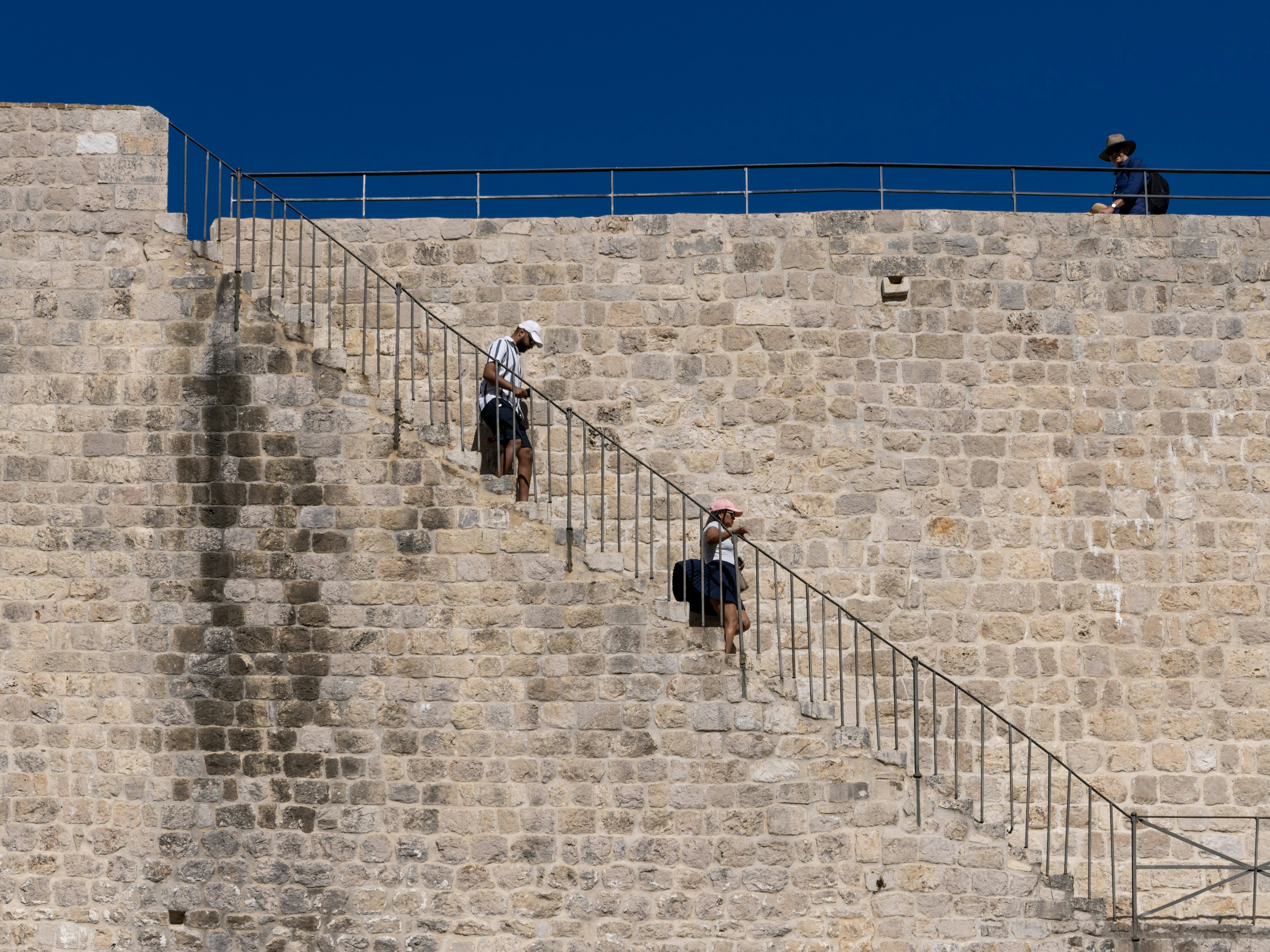 Stone Staircase Portrait: Climbers on a Historic Wall under a Clear Blue Sky