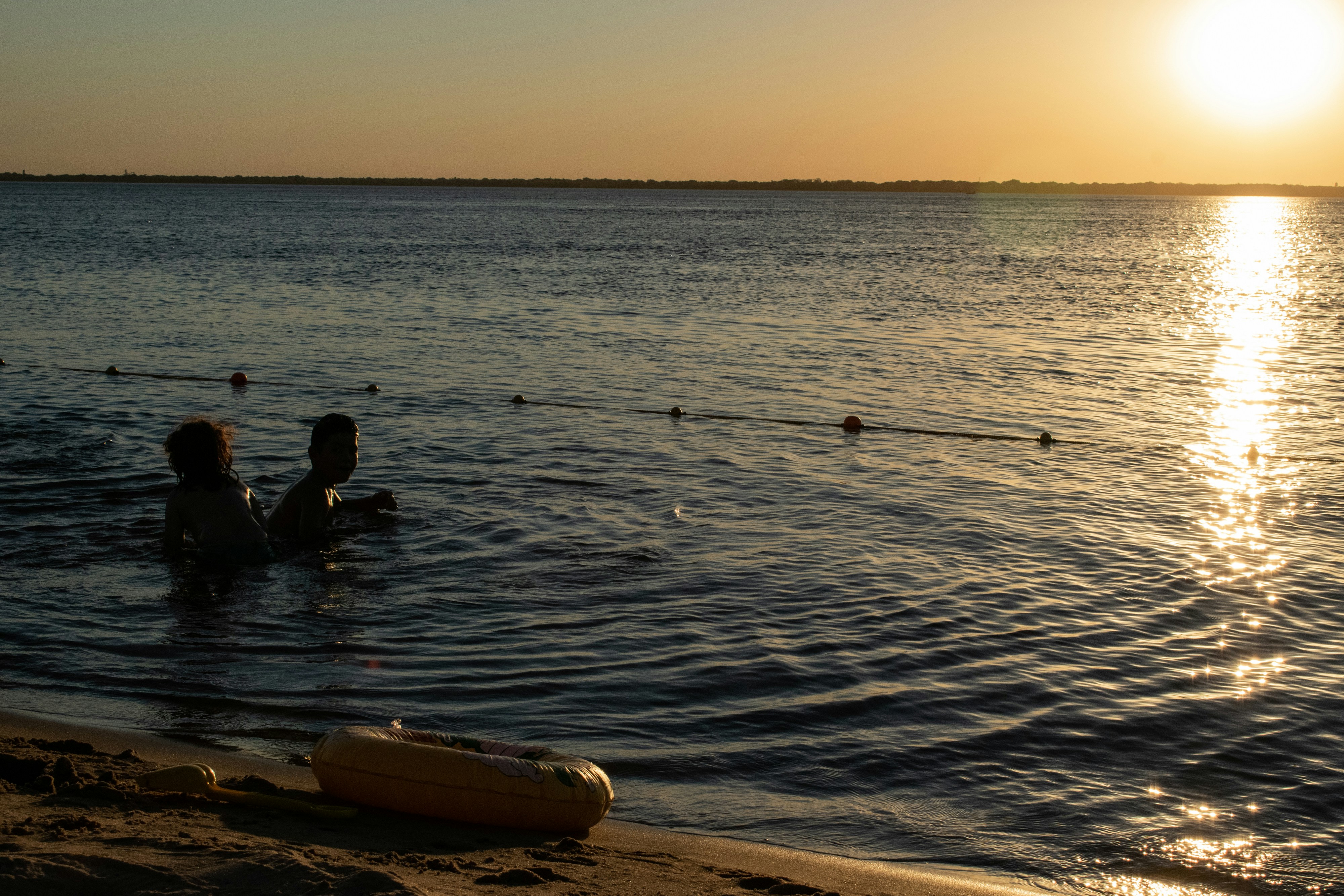 Sunlit shore swimmers at twilight with a rescue float resting on the sand