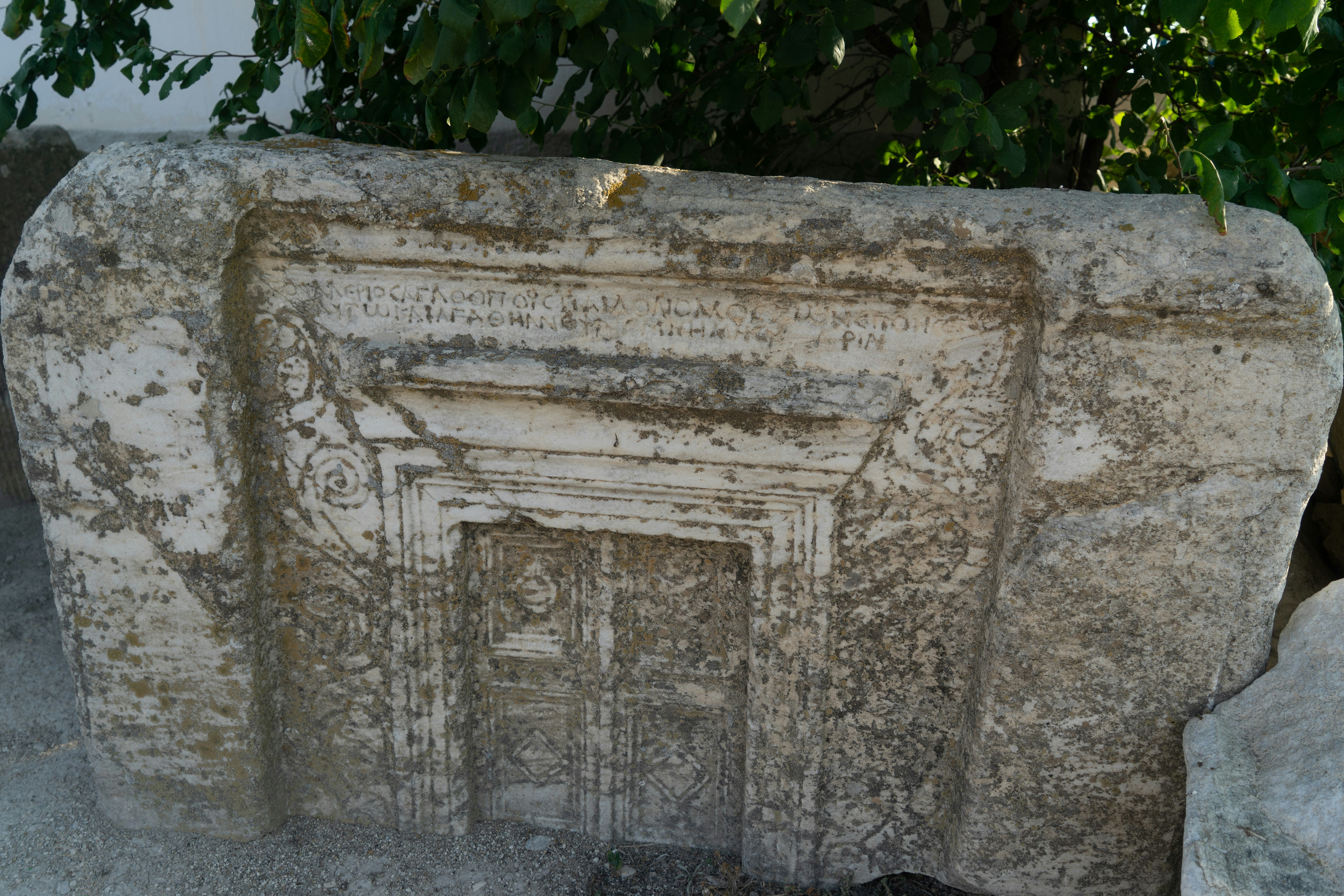 Ancient Stone Relic: Weathered Carved Panel Surrounded by Foliage