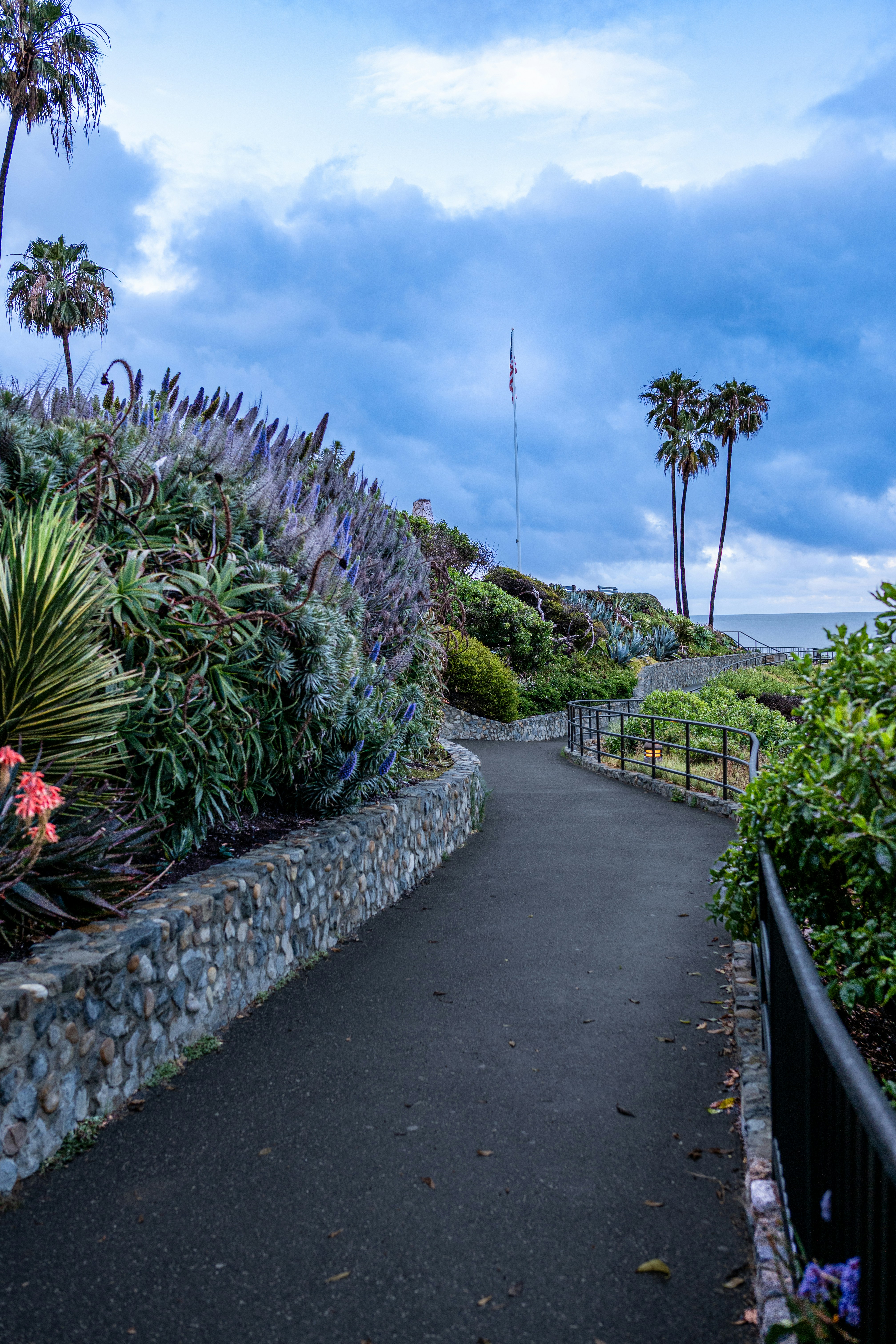 Stone path through a coastal garden toward the sea under a dramatic sky