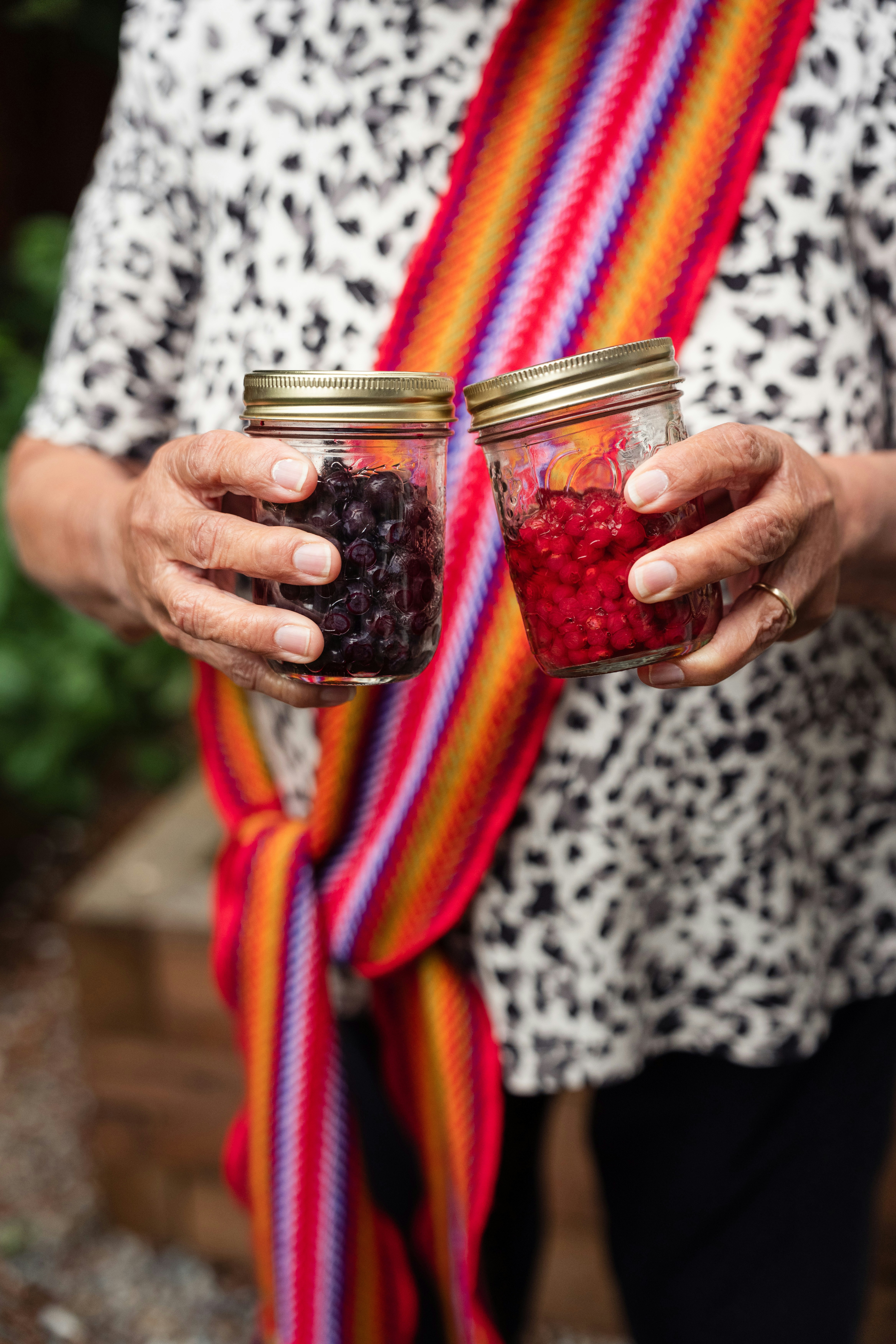 A person holding two glass jars filled with blueberries and red currants
