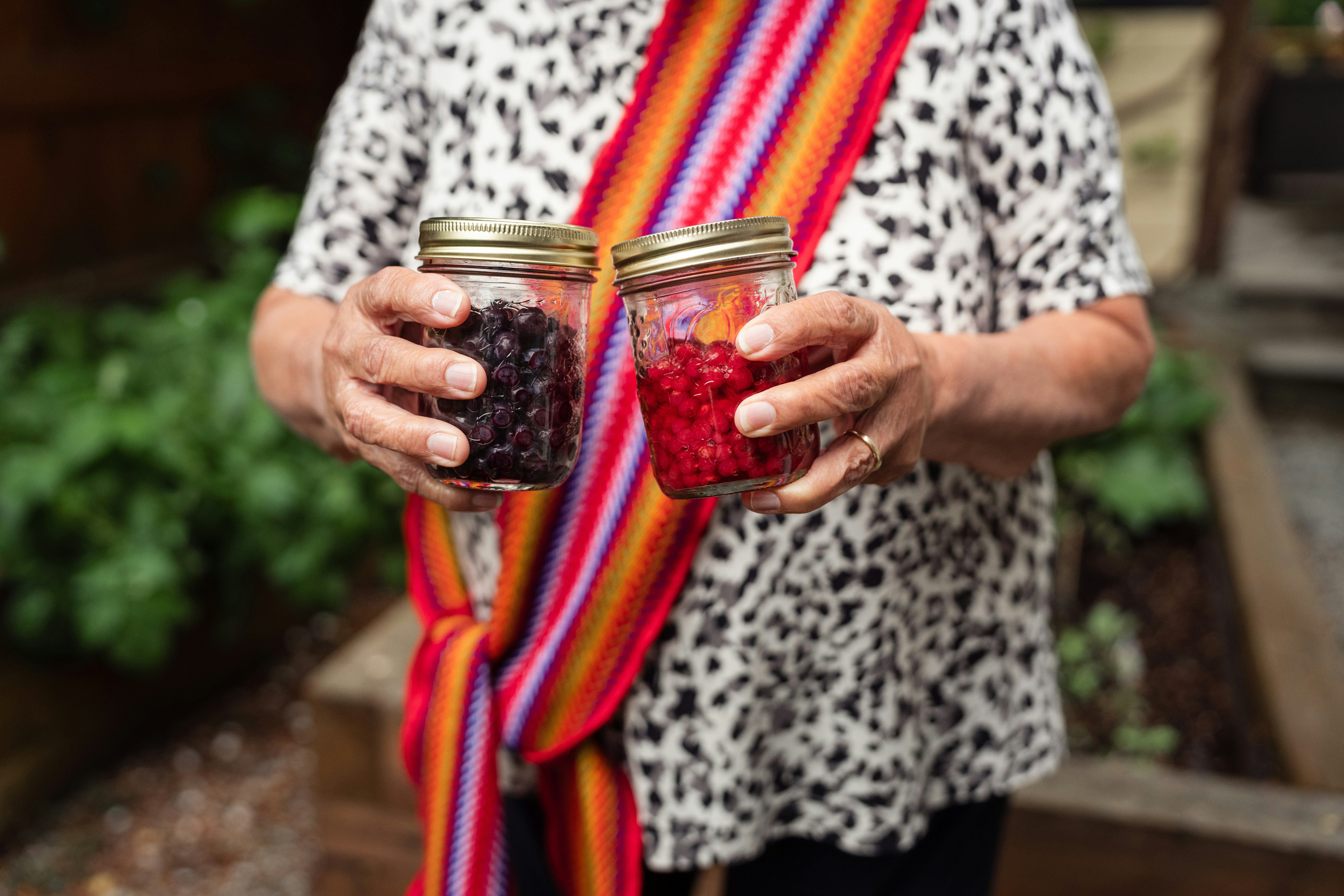 A person holding two glass jars filled with blueberries and red currants