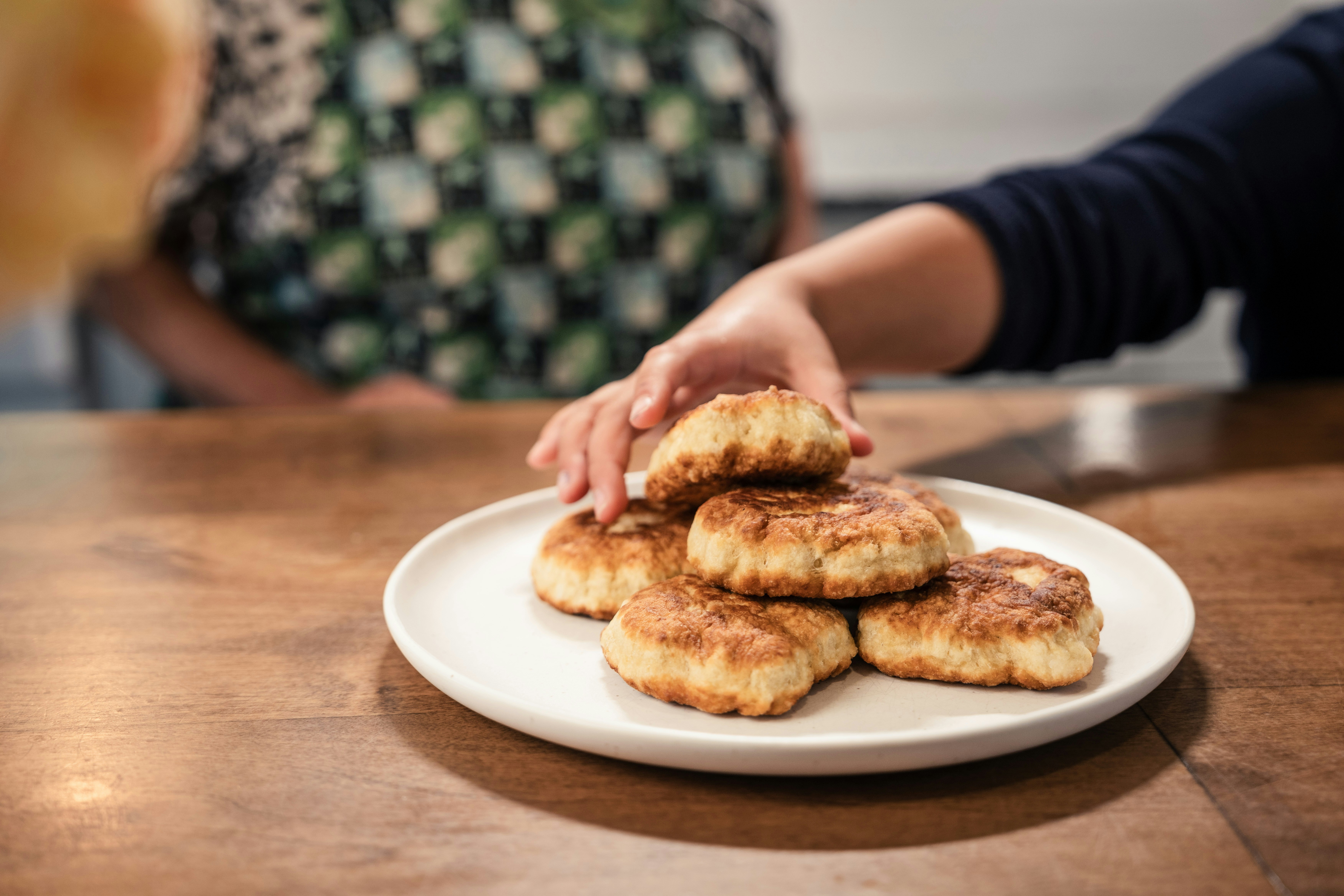 Hand Reaches for Stack of Golden Cookies on a Wood Table