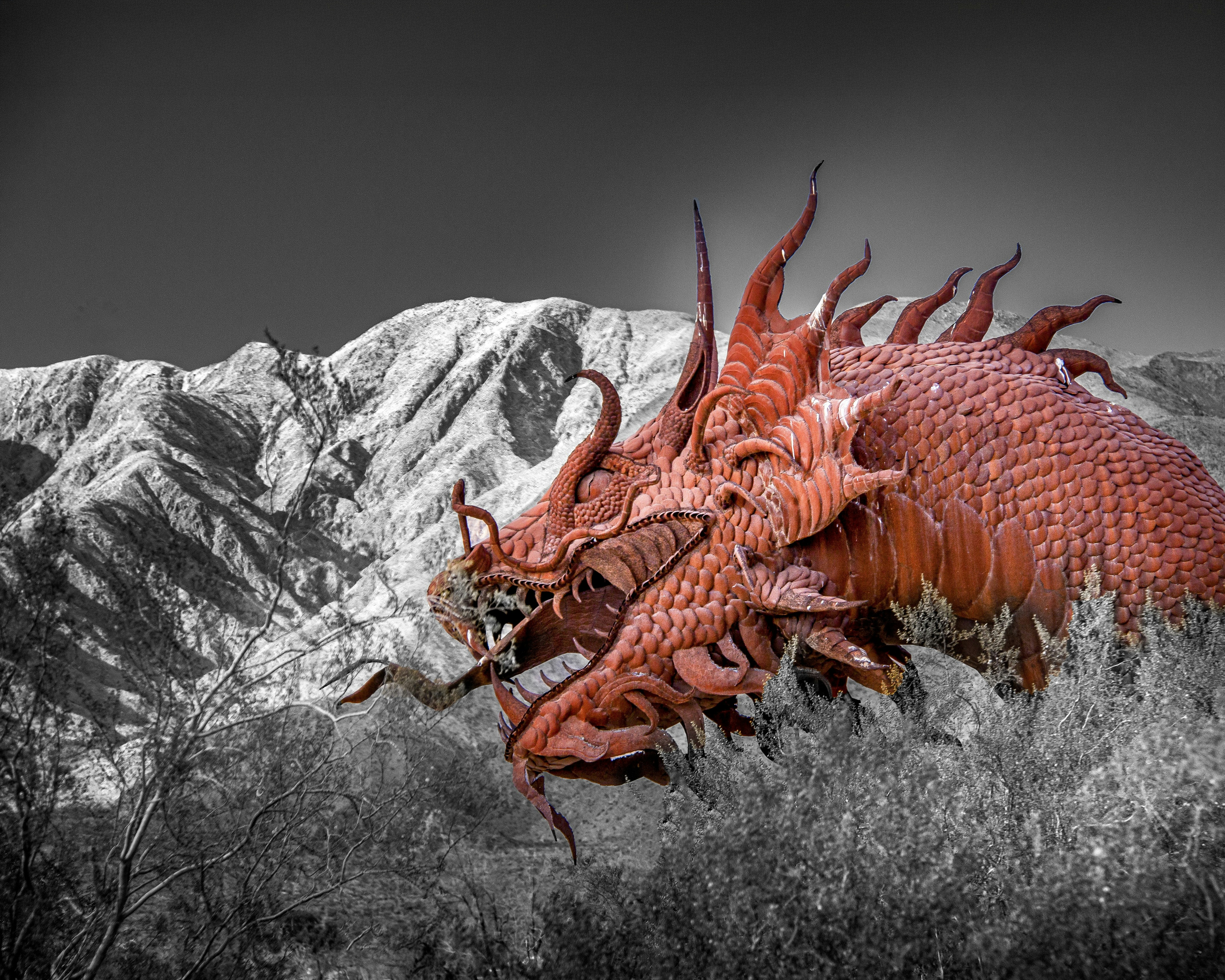 Scarlet dragon-like creature dominates a rocky hillside, set against a grayscale landscape, creating a stark color contrast and dramatic focal point.