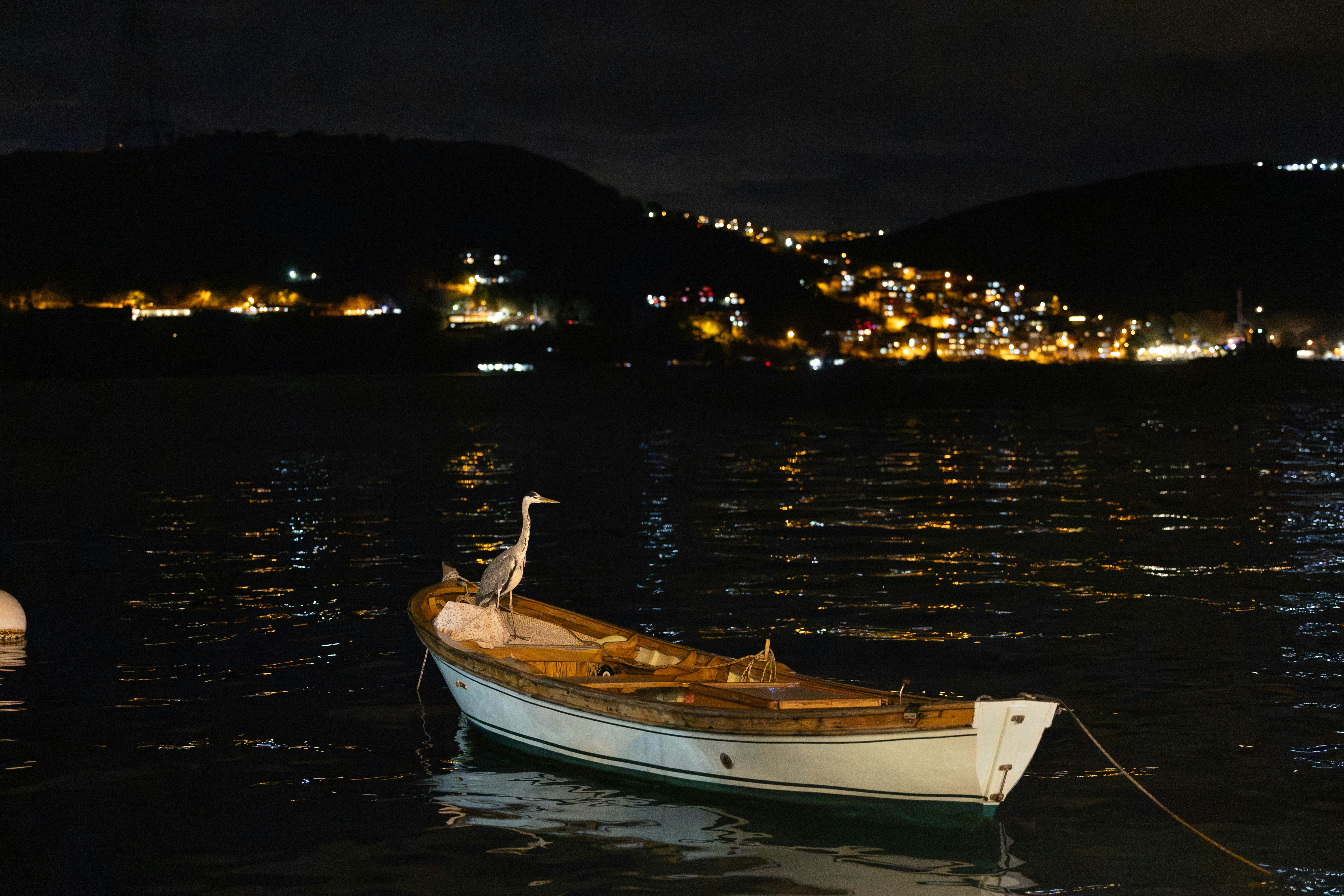 Moonlit Bow: A Lone Boat Anchored Beneath City Lights