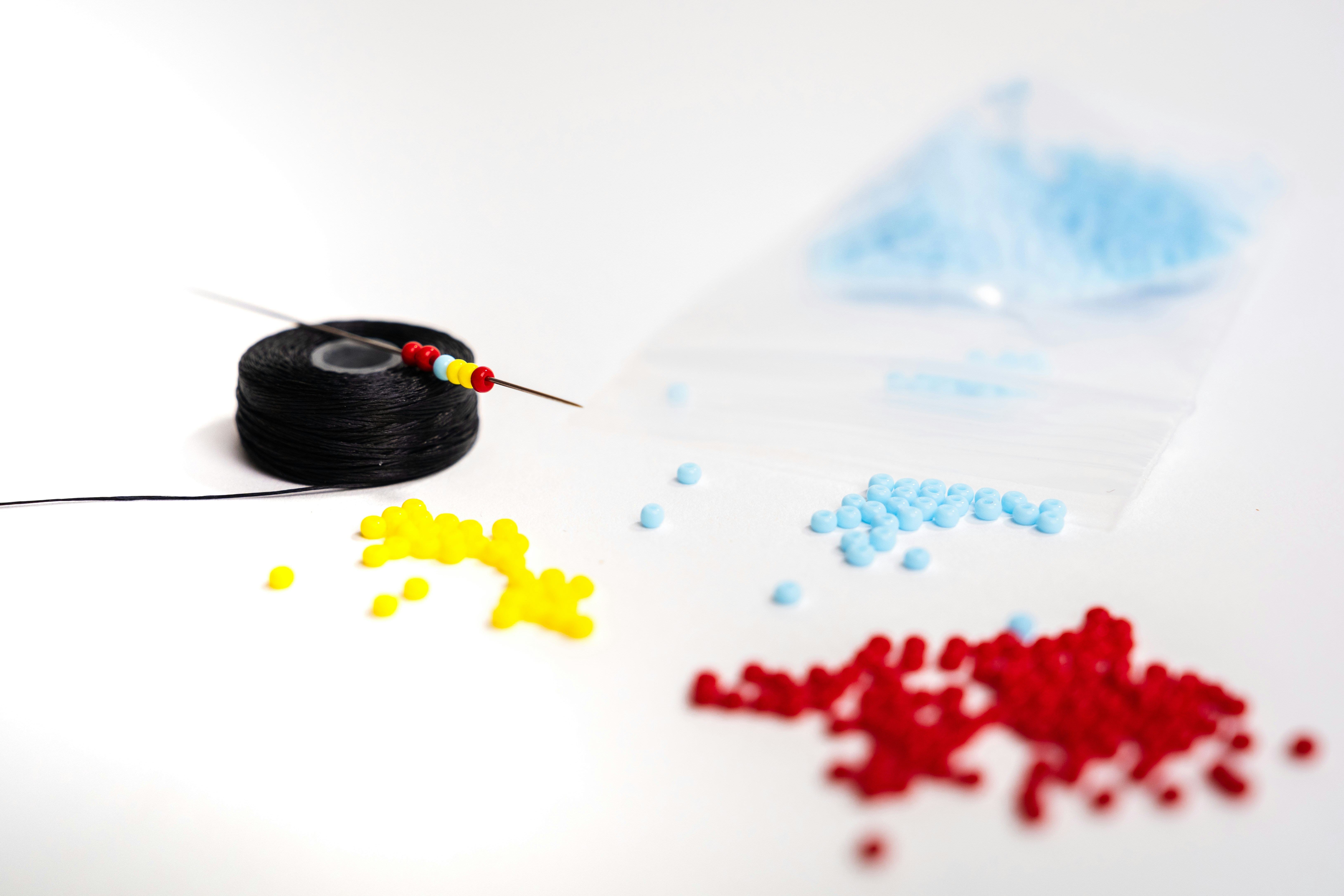 Spool of Black Thread with Assorted Color Beads on a White Studio Surface