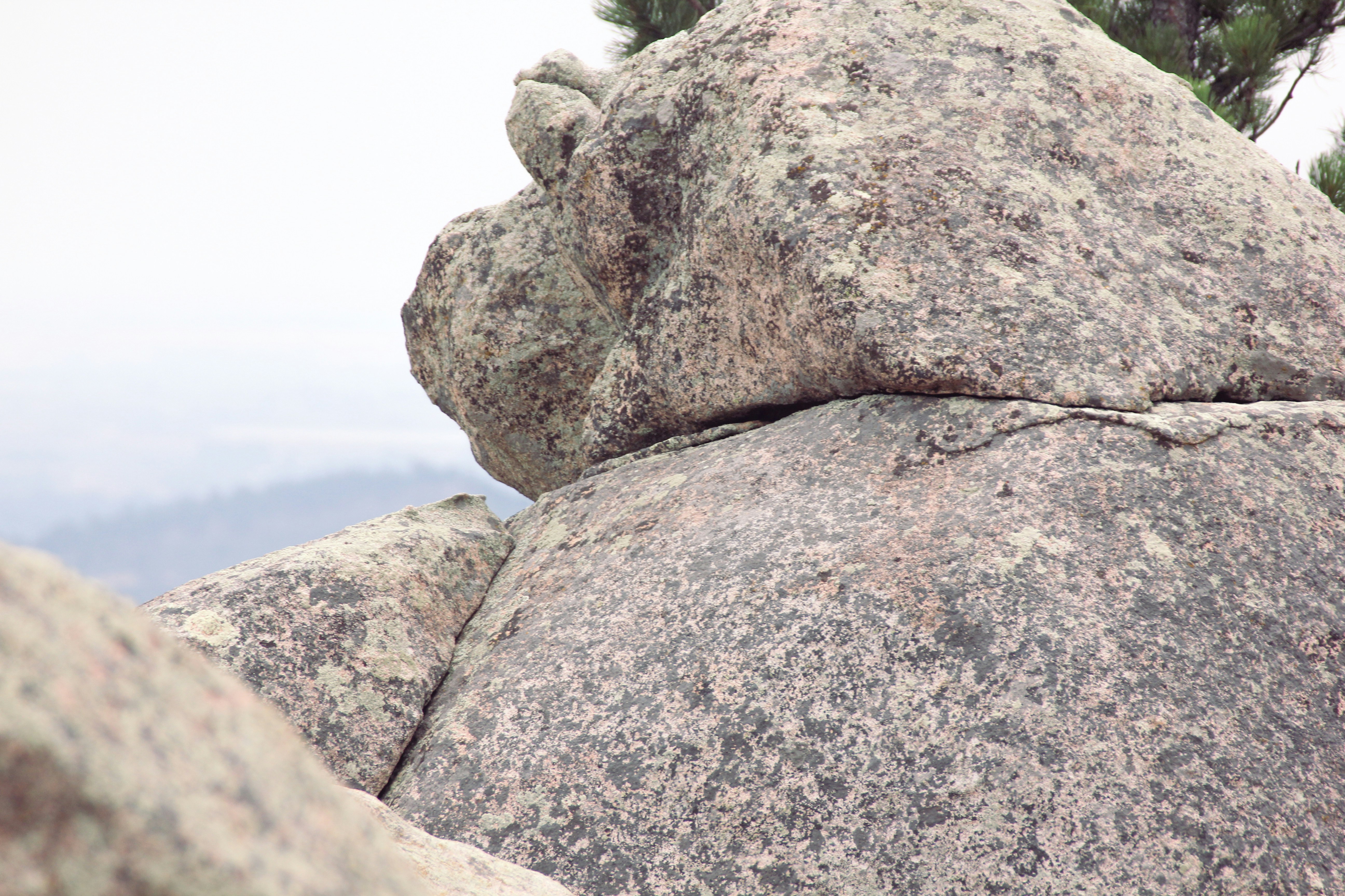 Rugged granite boulders dominate the frame with a distant, hazy horizon peeking through; the texture and contrast emphasize the rock's weathered surface. A close-in landscape detail focused on geological form.