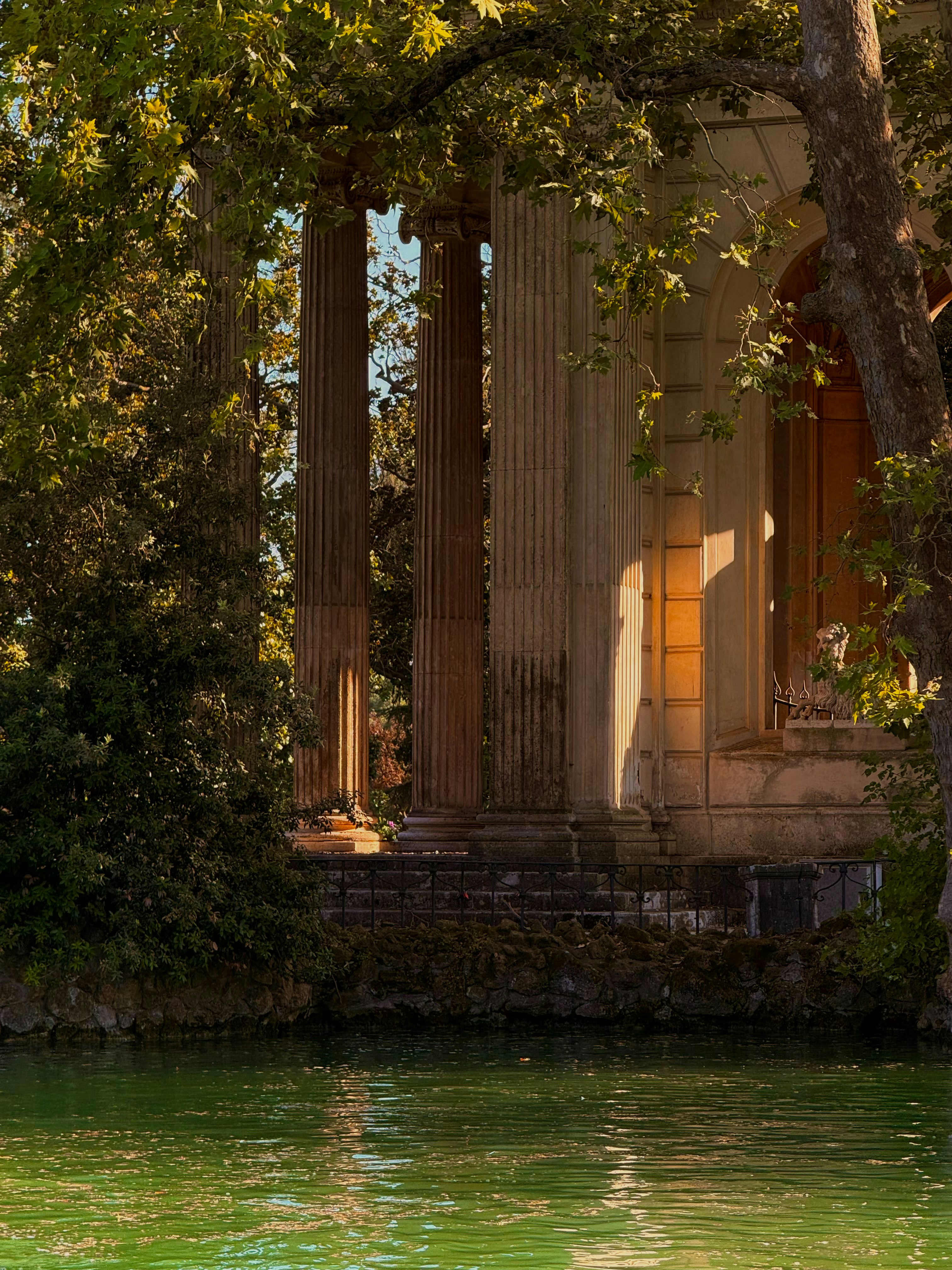 Ancient Columns by the Water: Sunlit Facade Framed by Trees
