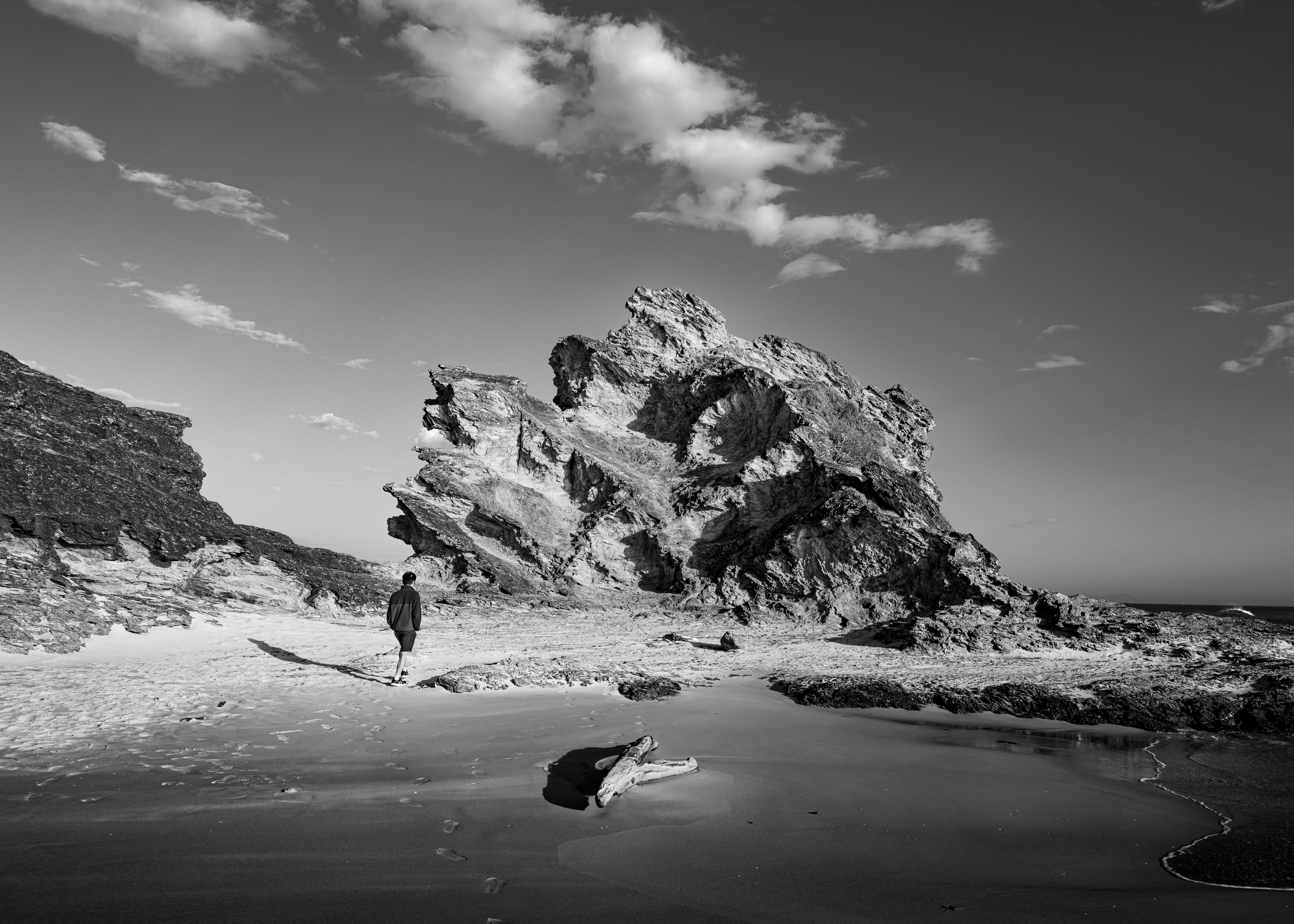 Footprints at the Edge: Man Walks Toward a Coastal Rock Form