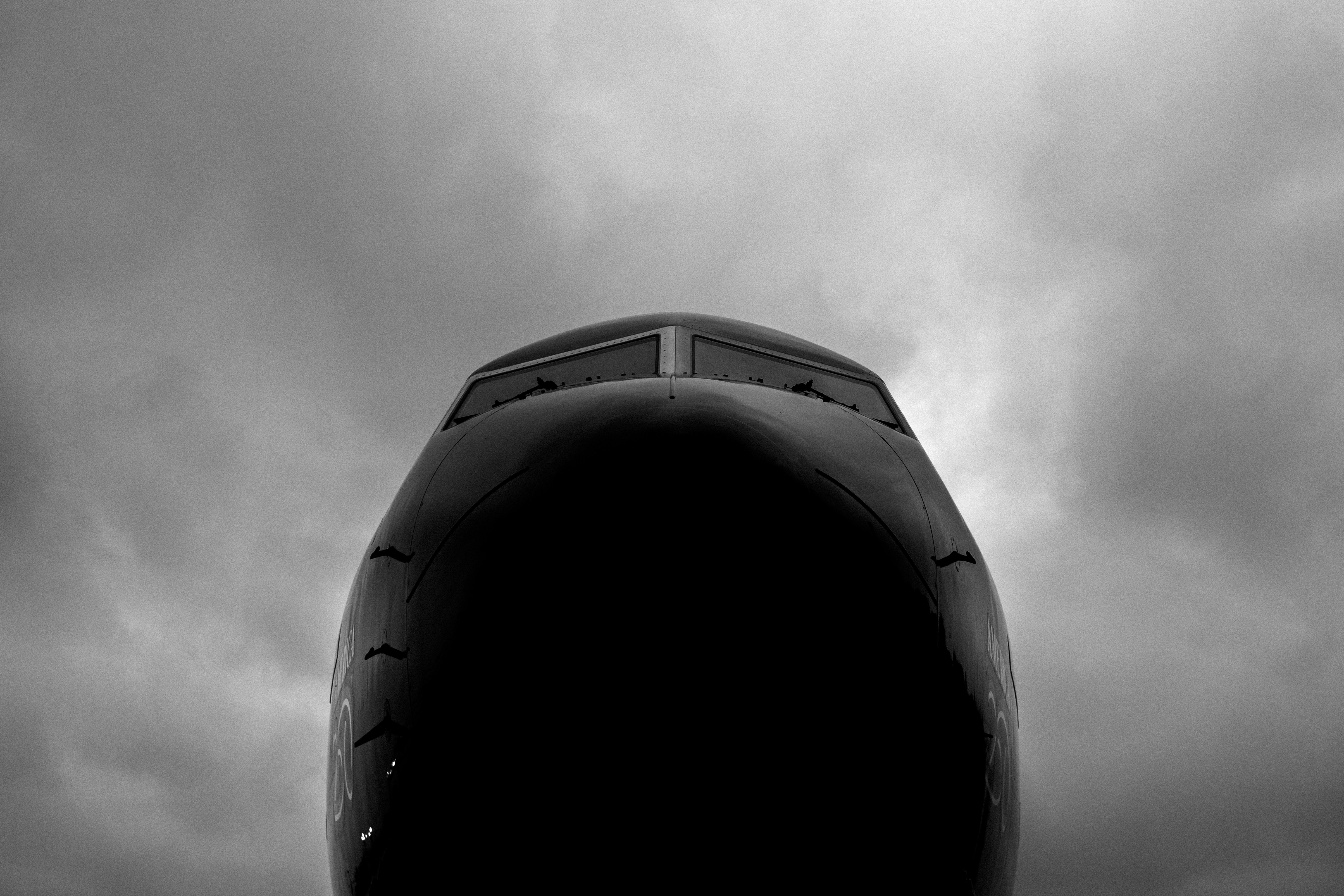 Jet nose pointed toward the camera against a cloudy sky, emphasizing dramatic silhouette and symmetry. A monochrome capture focusing on the aircraft’s forward body and looming canopy.