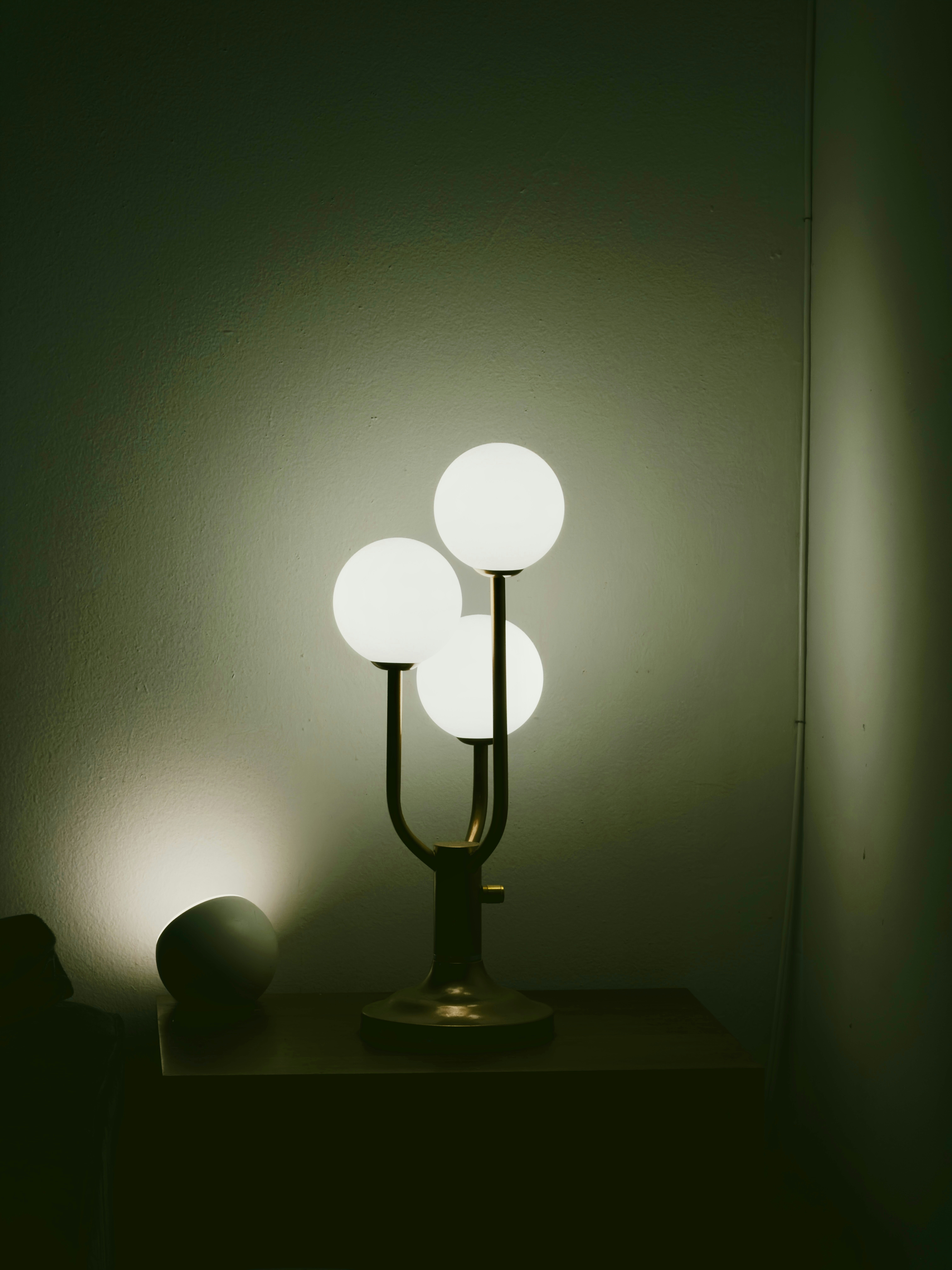 A three-globe brass lamp glowing on a wooden surface against a wall