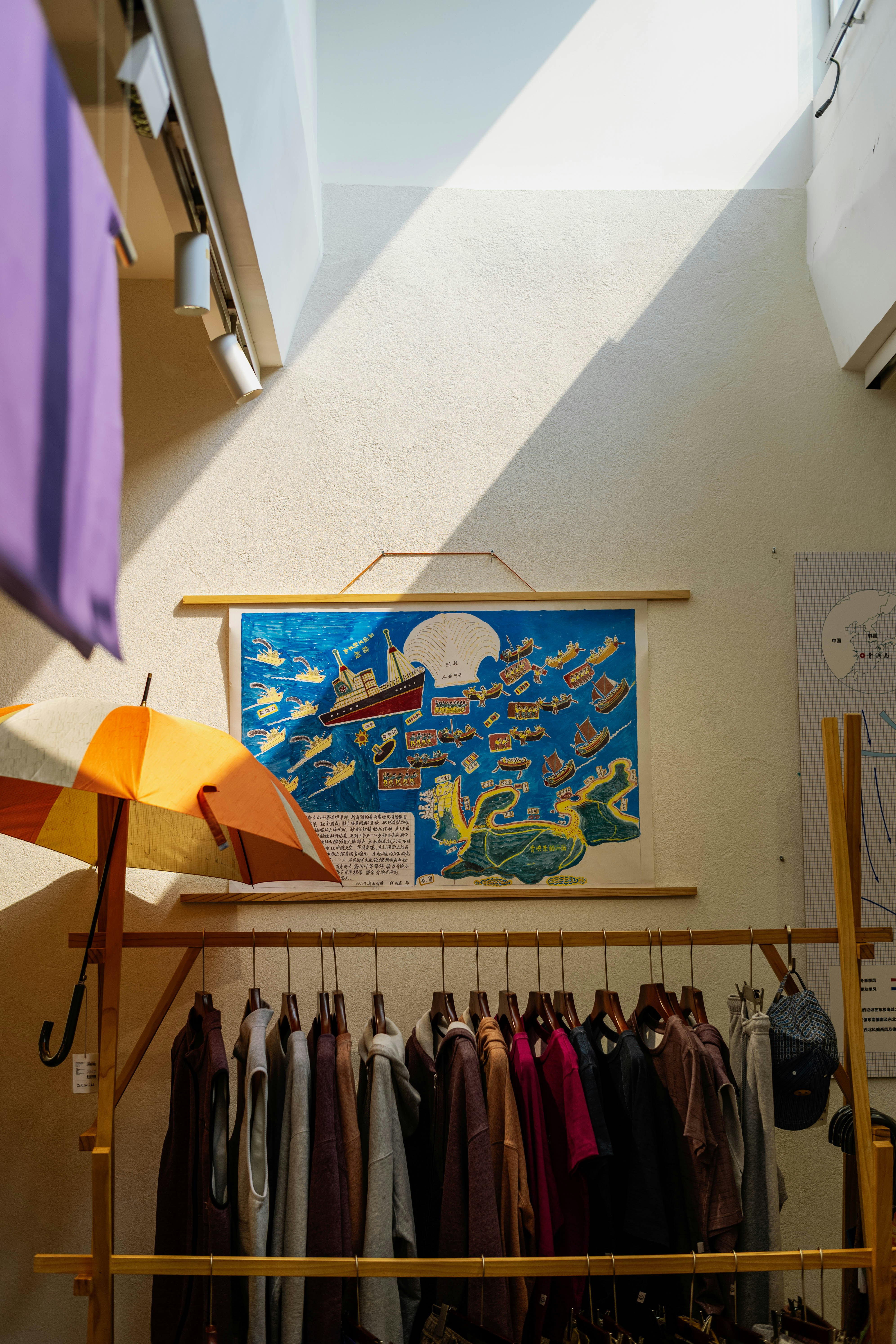 Sunlit Gallery: A Rack of Garments Beneath a Colorful Map