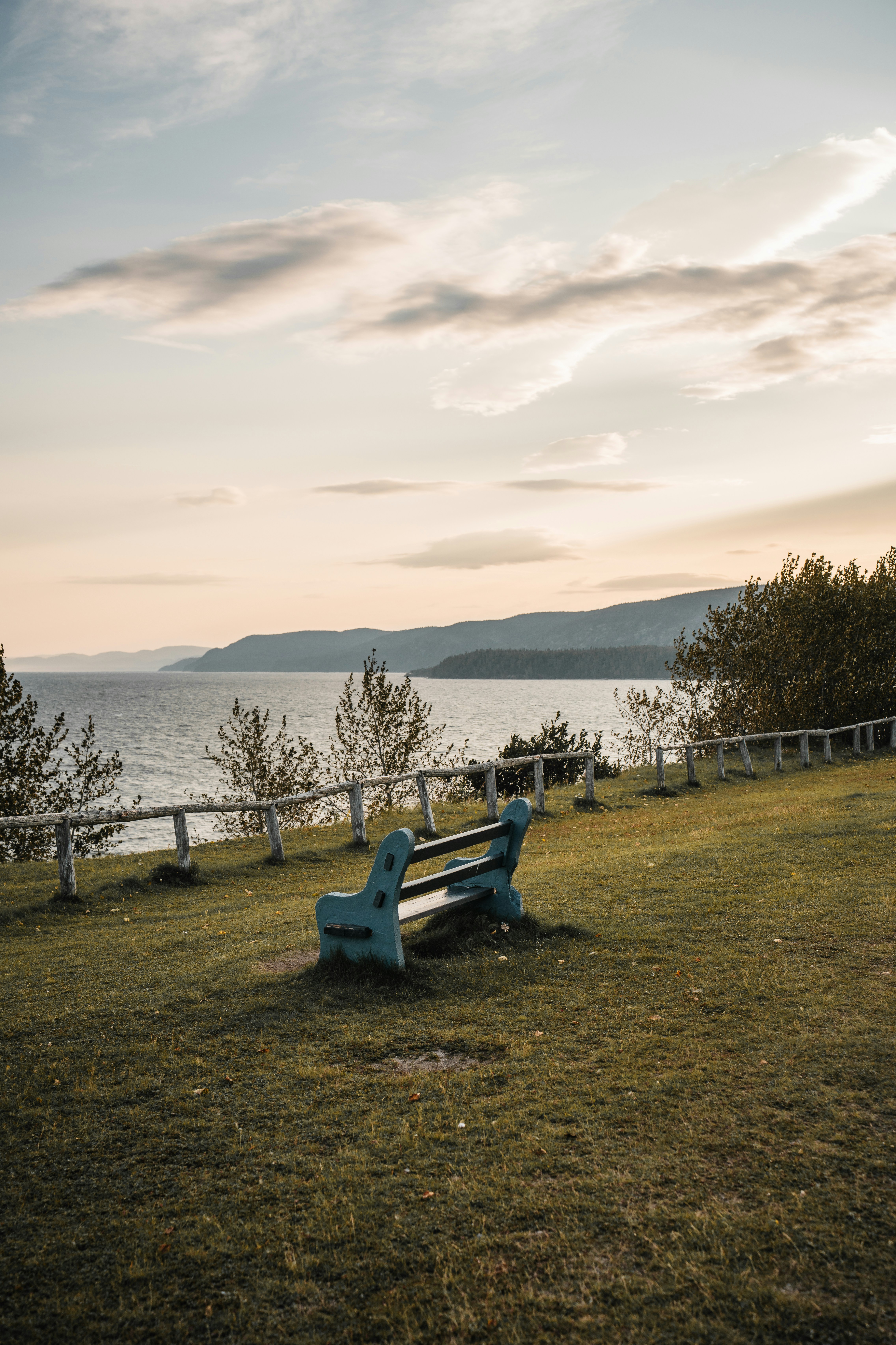 Blue bench by the shoreline under a soft sunset sky