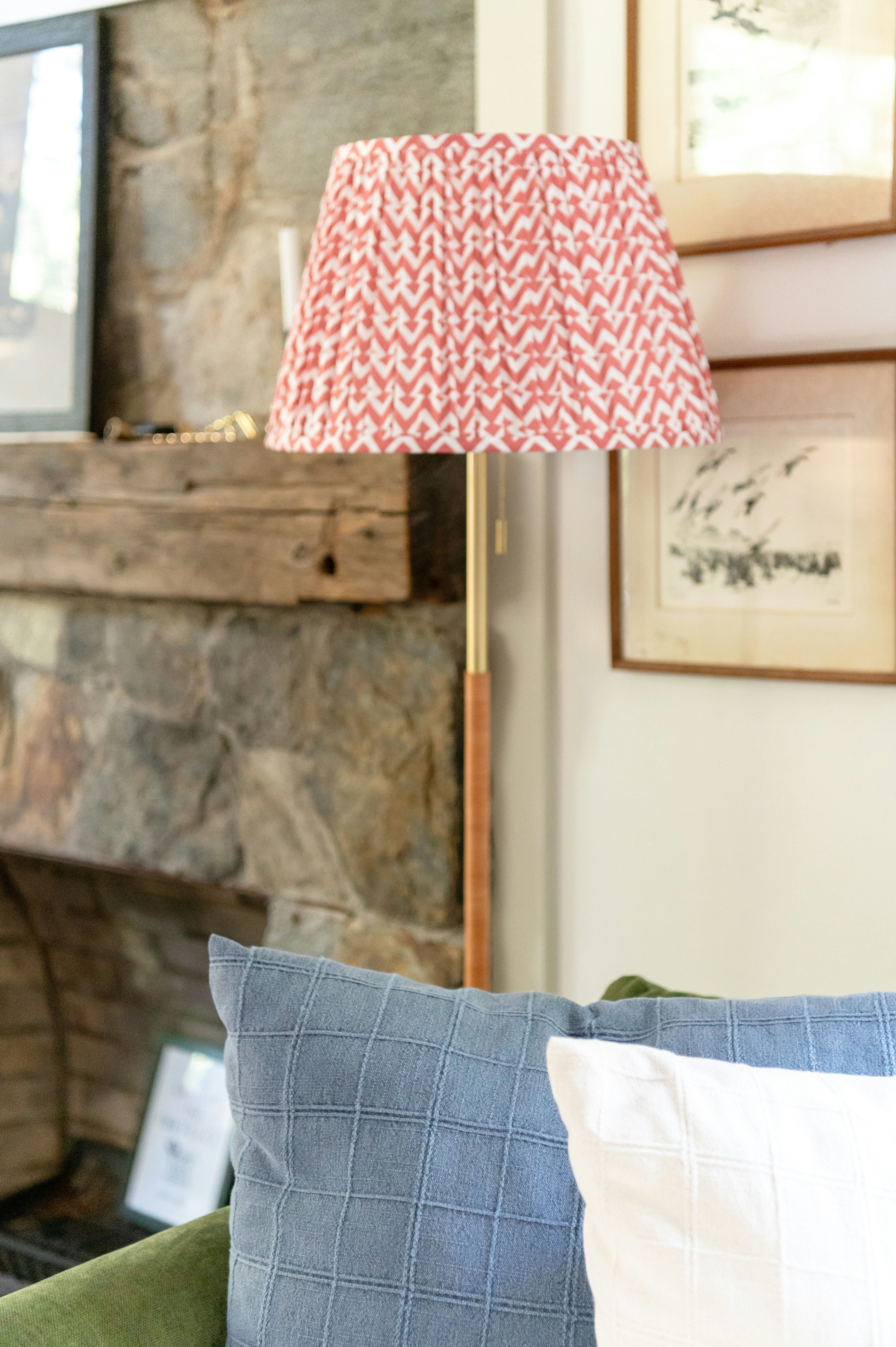 Cozy living room scene featuring a red chevron-pattern lamp shade above a blue cushion on a green sofa, with a stone fireplace and framed art in the background.