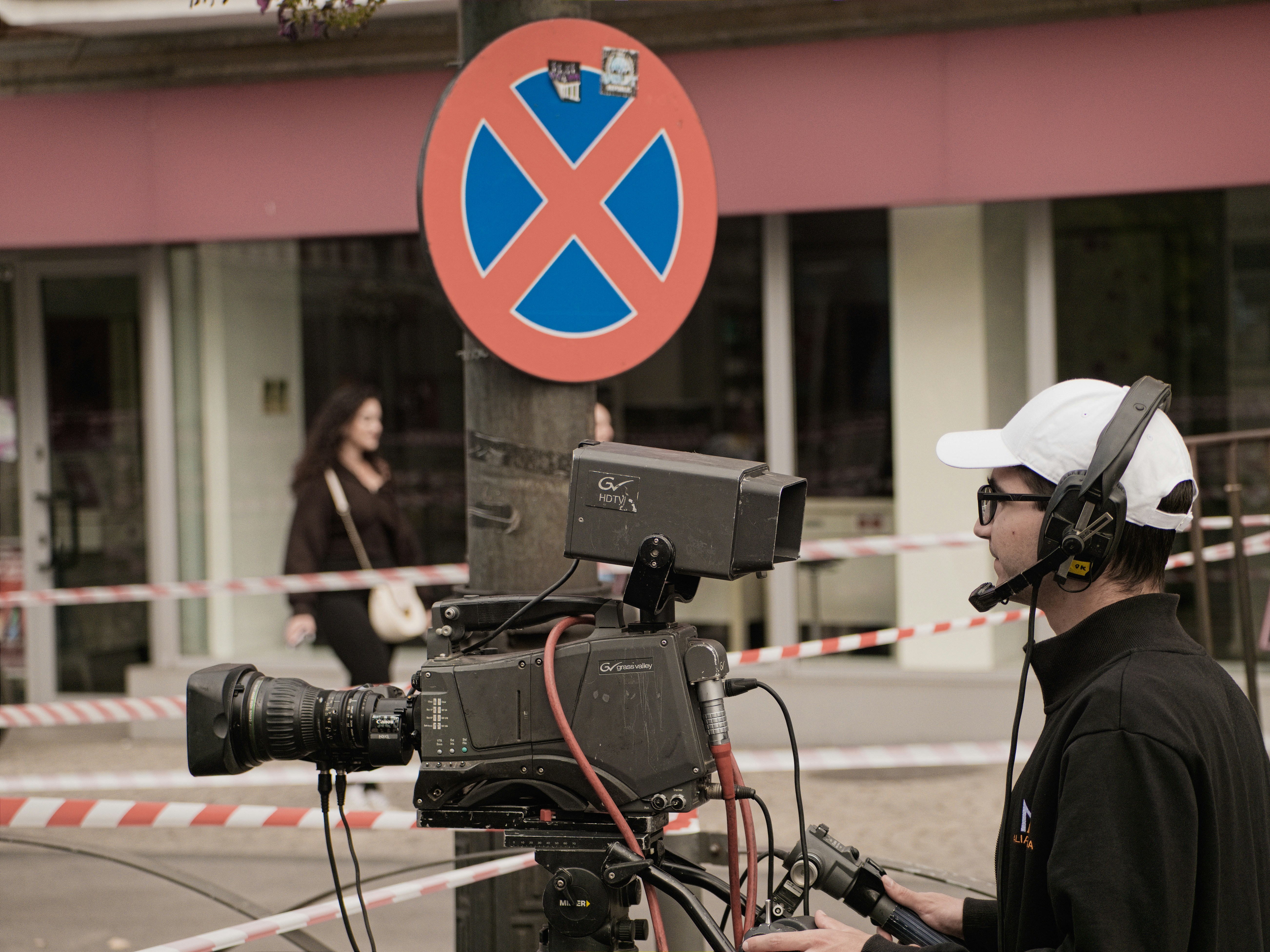 Two filmmakers and a digital cinema setup dominate a cordoned street scene with a prominent no-parking sign in the background.