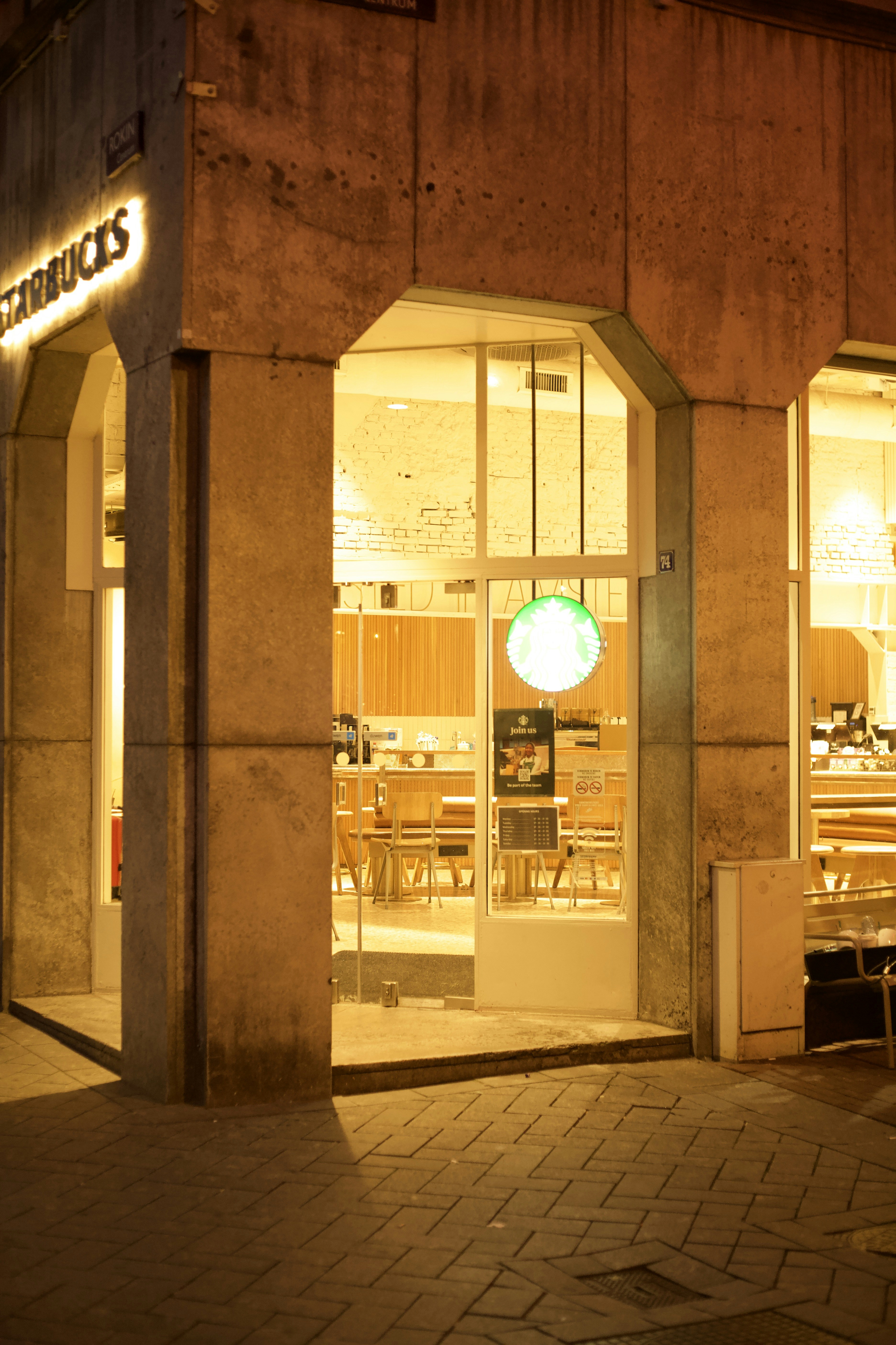Neon Green Halo: Inside a Warmly Lit Starbucks through Concrete Arches