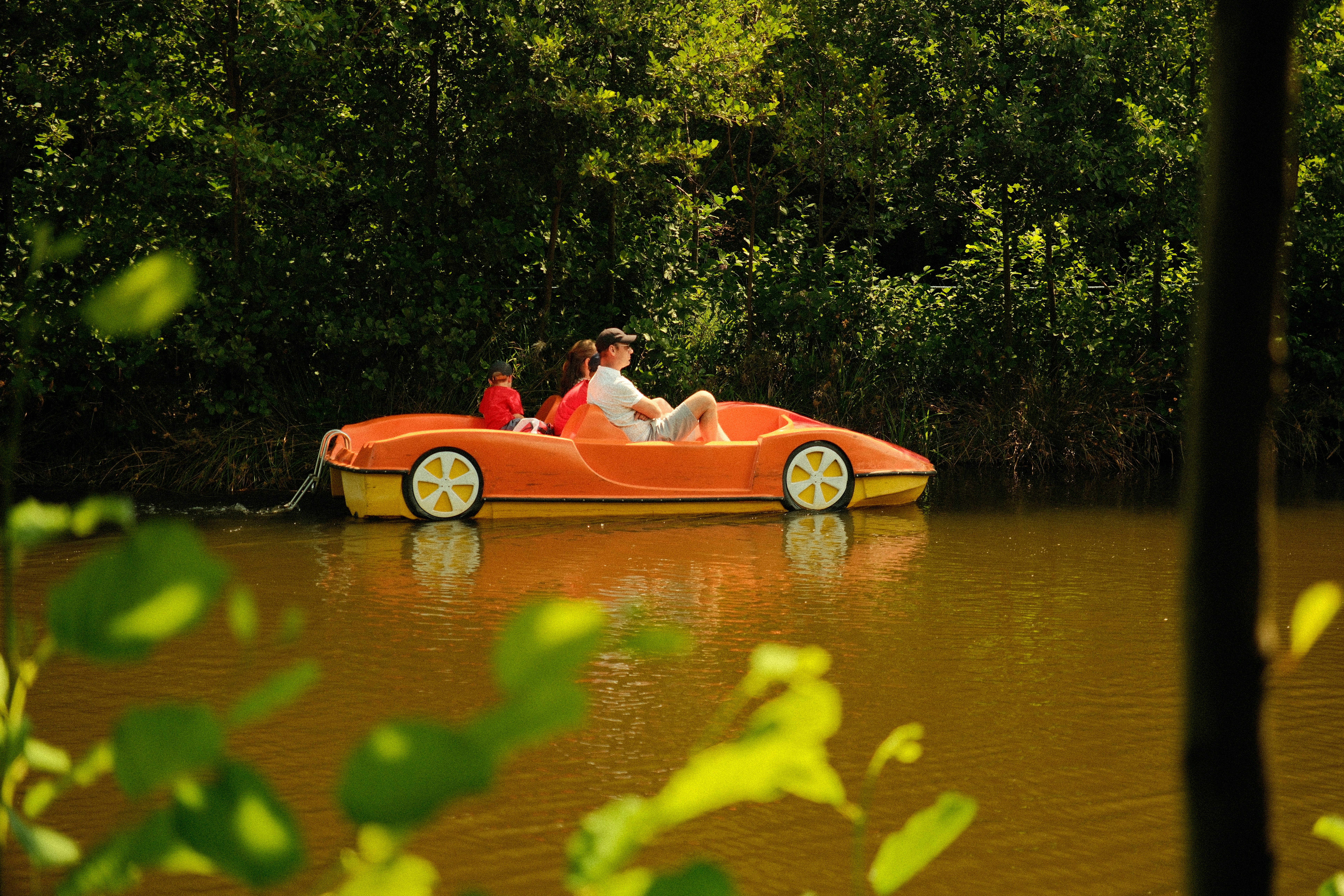 Orange pedal boat gliding along a sunlit river