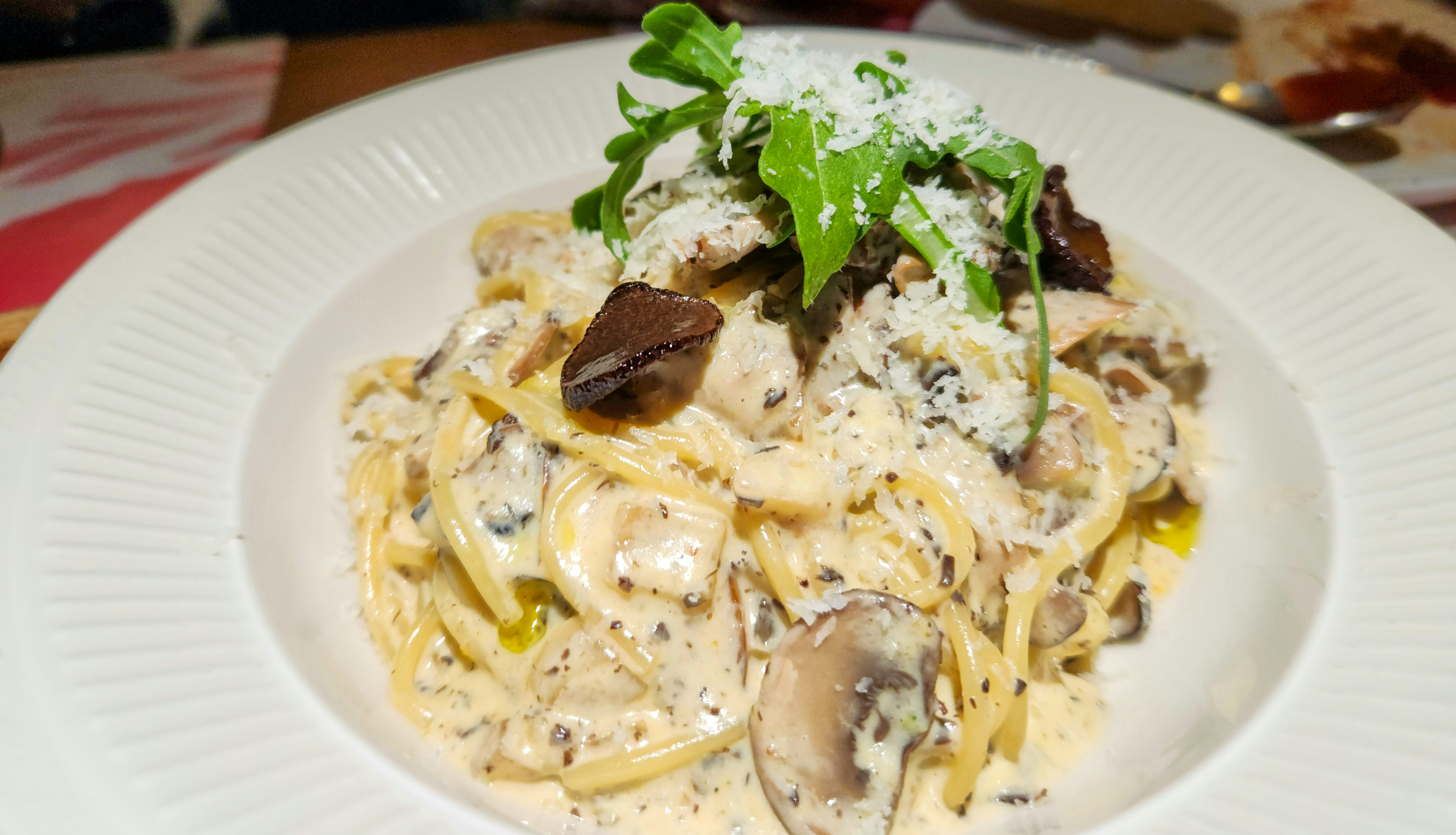 Creamy mushroom pasta with sliced mushrooms and herbs plated on a white dish. A fresh greens garnish sits atop the pasta, adding color and contrast.