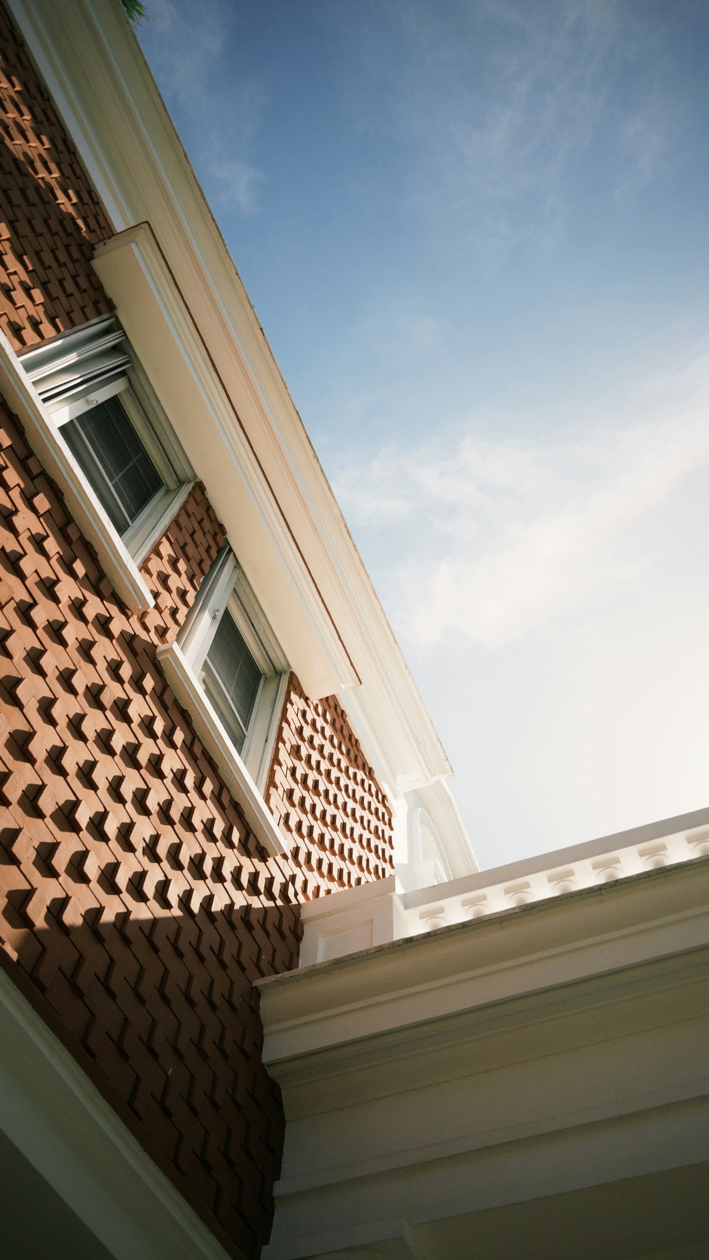 Sunlit brick facade and white cornice form dramatic angles along a corner, with a clear blue sky above.