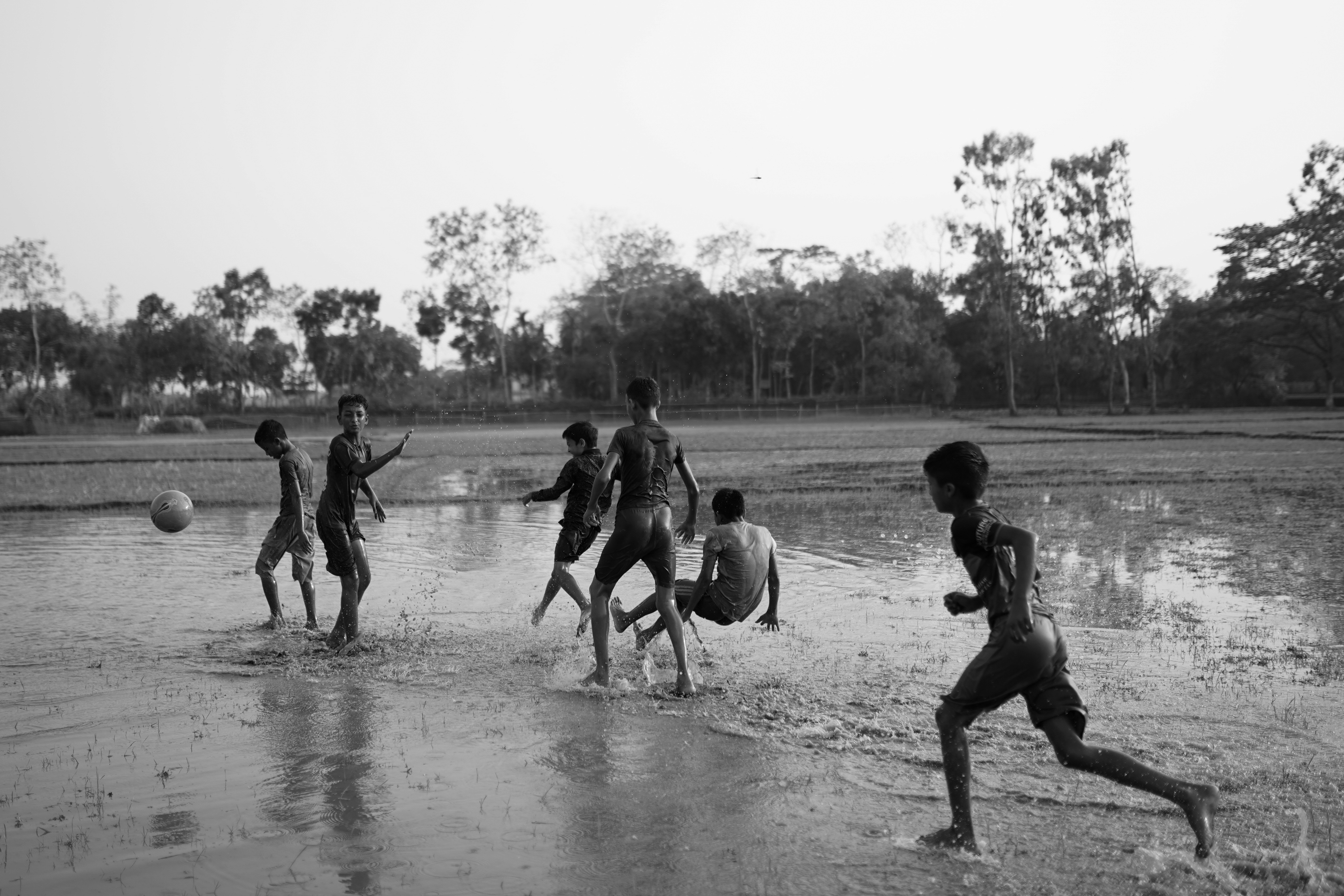 Mud field soccer: children chase a bouncing ball at dusk