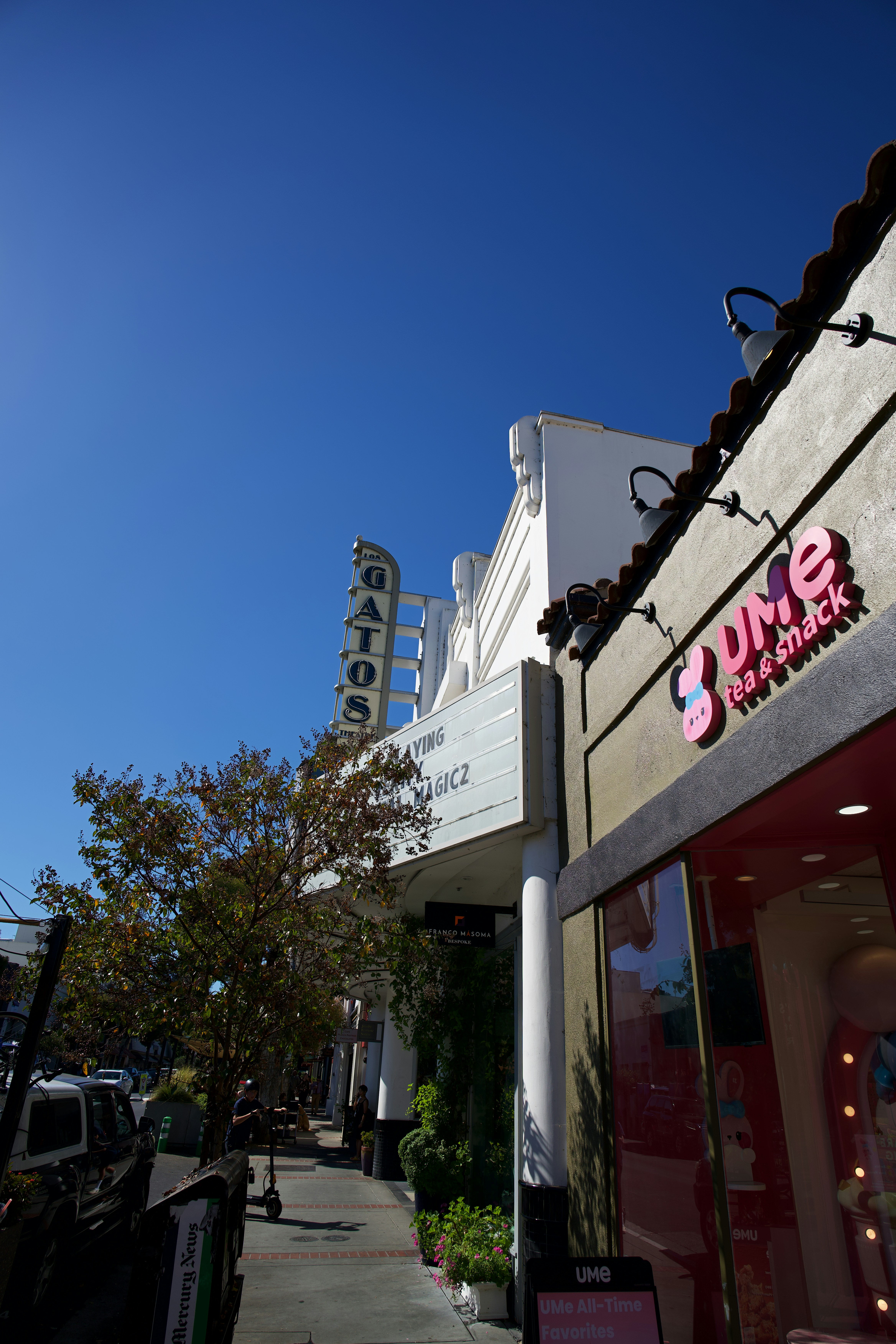Sunlit Streetfront with Neon Sign and Shadowed Pedestrian Walk