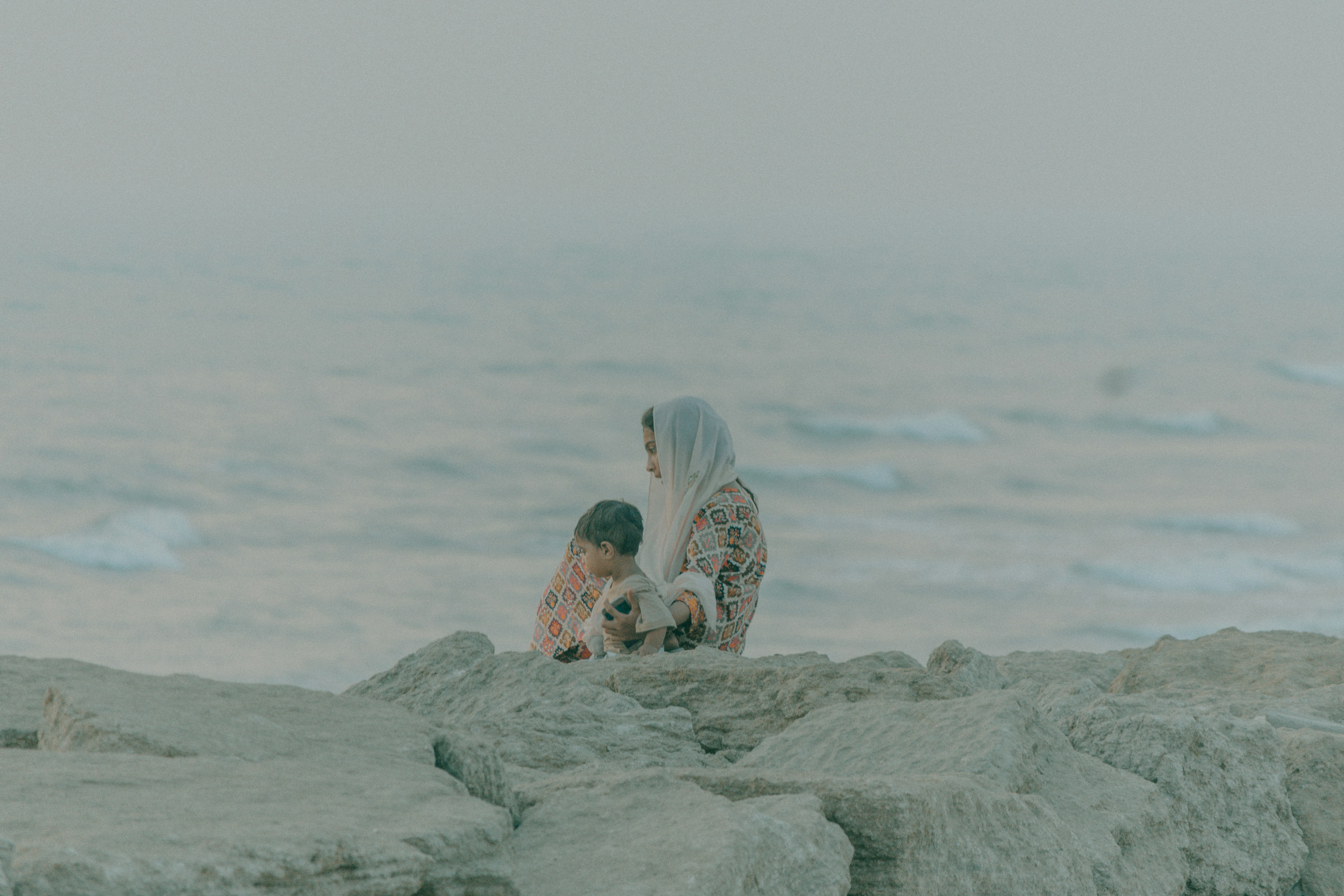 Quiet Shoreline: A Mother and Child Amidst the Lichen-tinged Rocks
